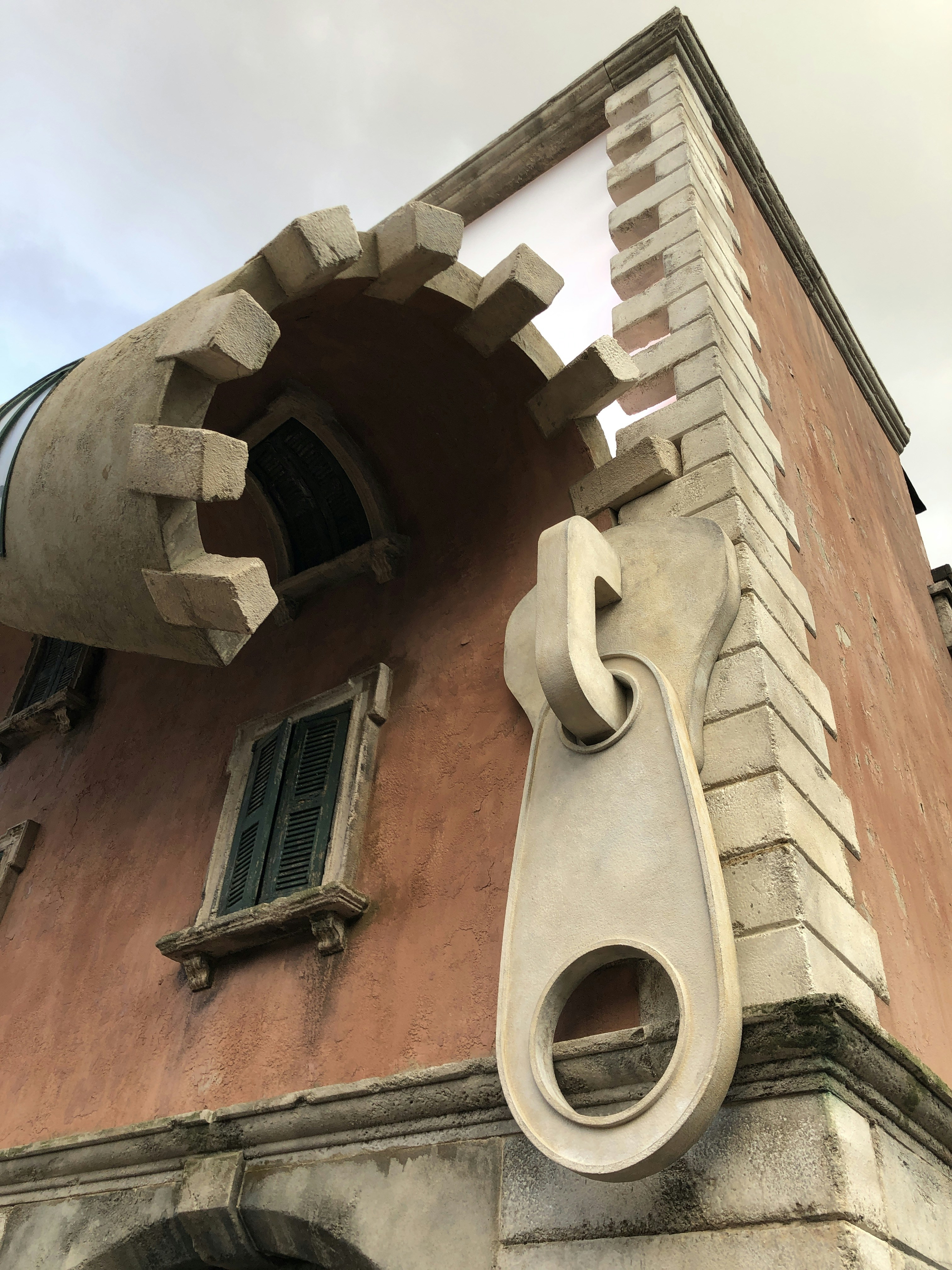 A whimsical building facade featuring a giant zipper and a broken circular section, blending art and architecture in a unique way.