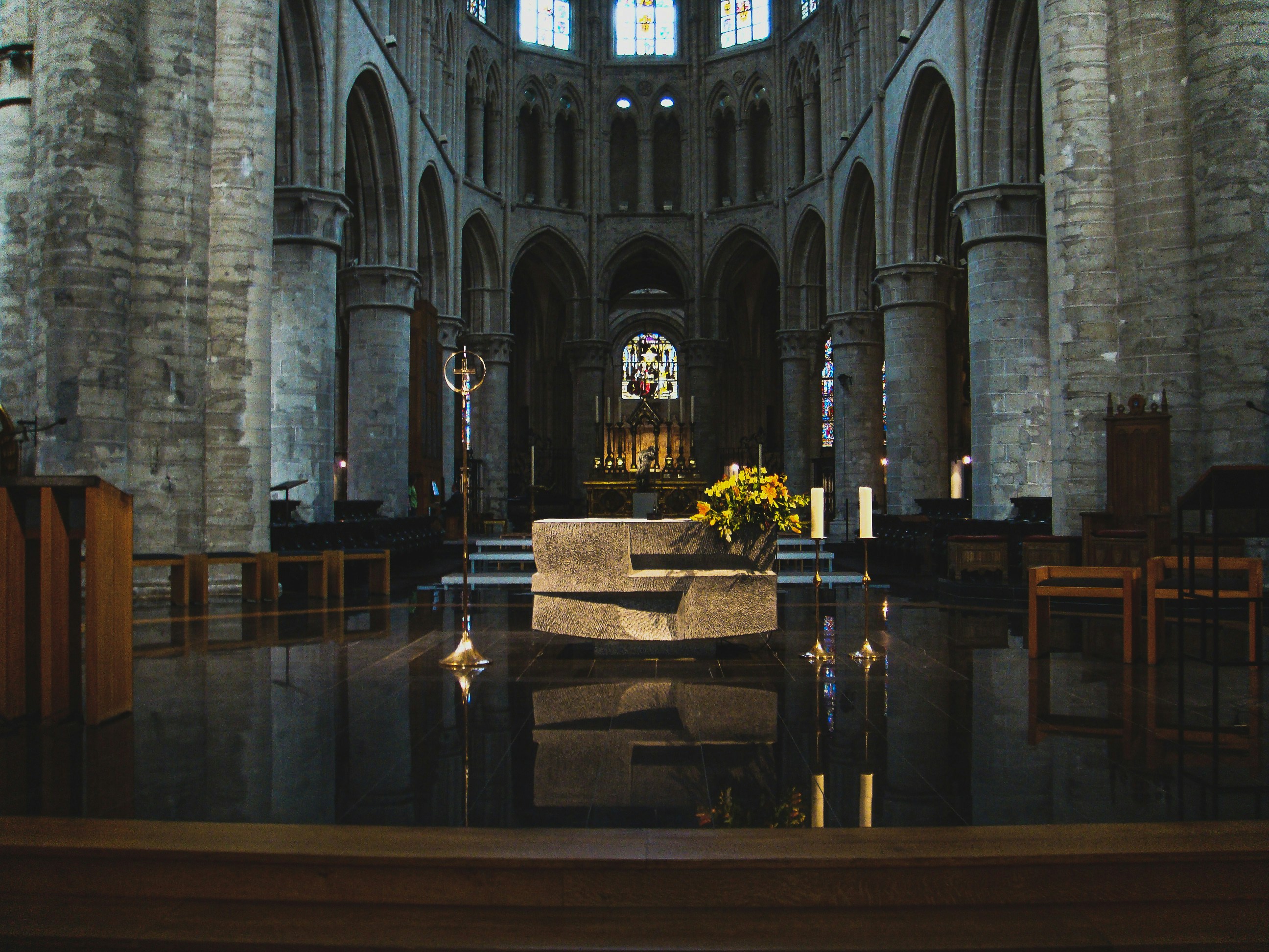 Interior of a grand cathedral featuring a central altar adorned with flowers, surrounded by towering stone columns and stained glass windows.