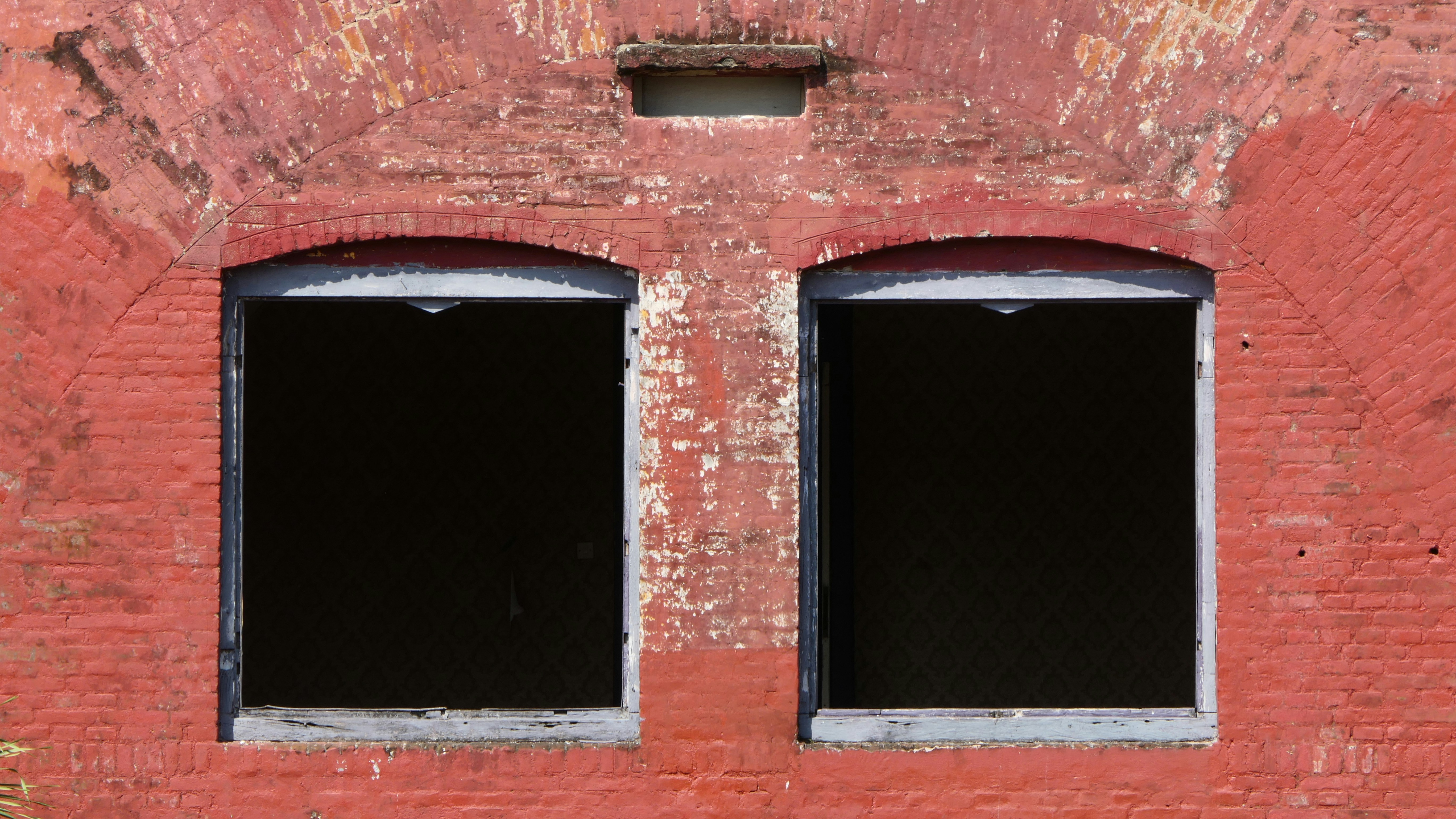 Weathered red brick wall featuring two empty arched windows, showcasing the passage of time and neglect.