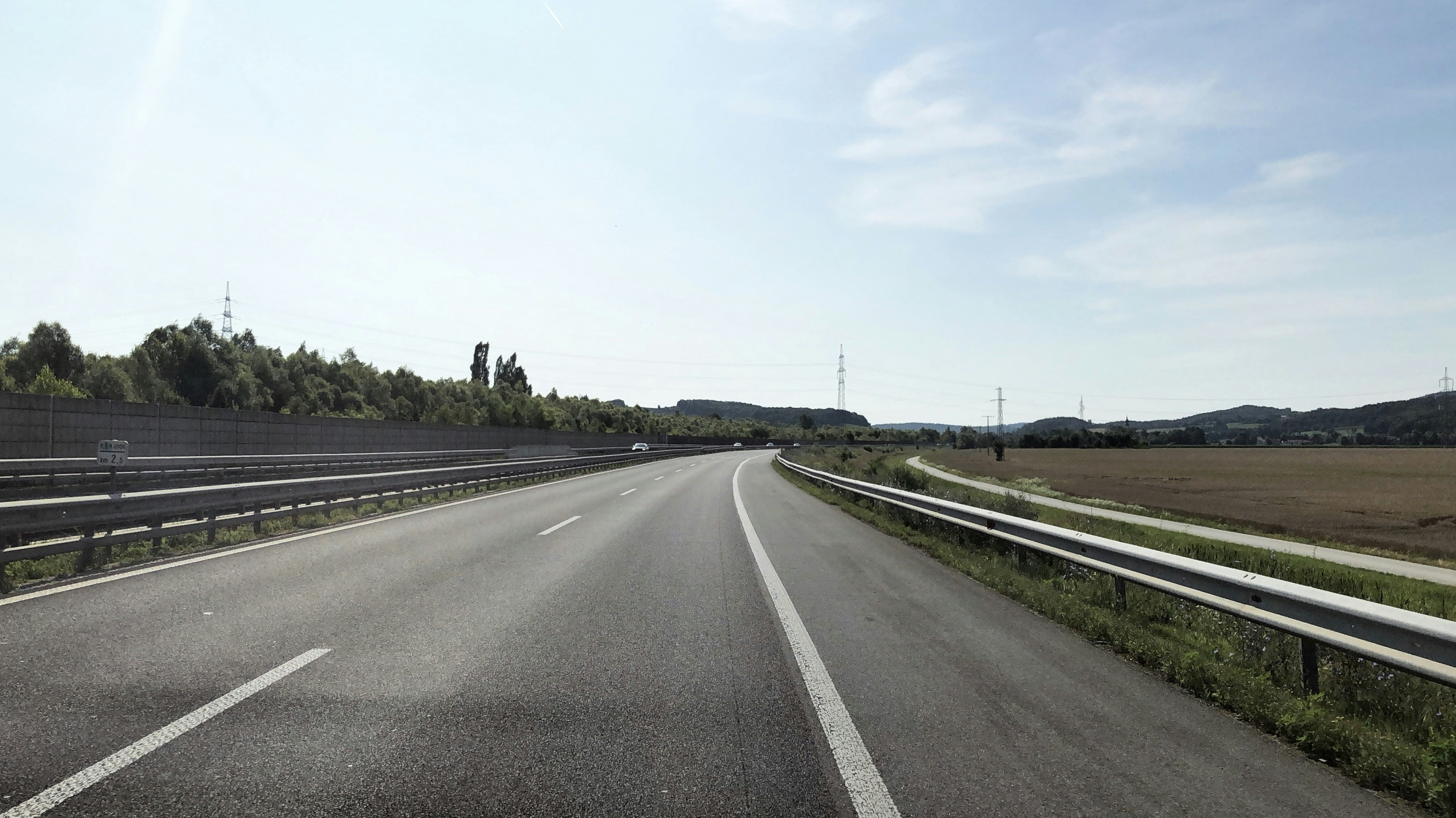 Curving highway surrounded by lush greenery and distant hills under a clear sky.