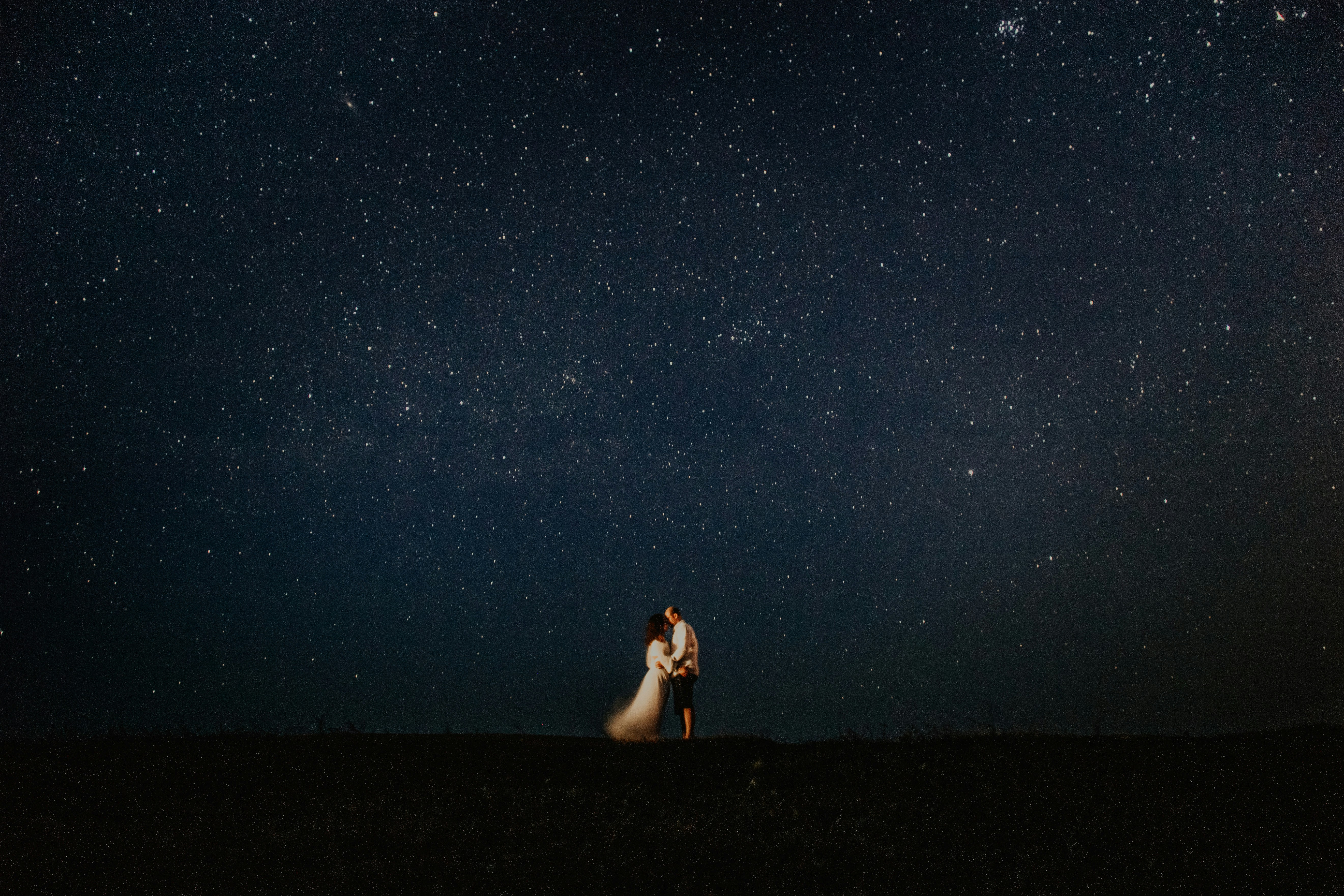 Couple sharing a romantic moment against a backdrop of a star-filled night sky. The vastness of space enhances the intimacy of their connection.