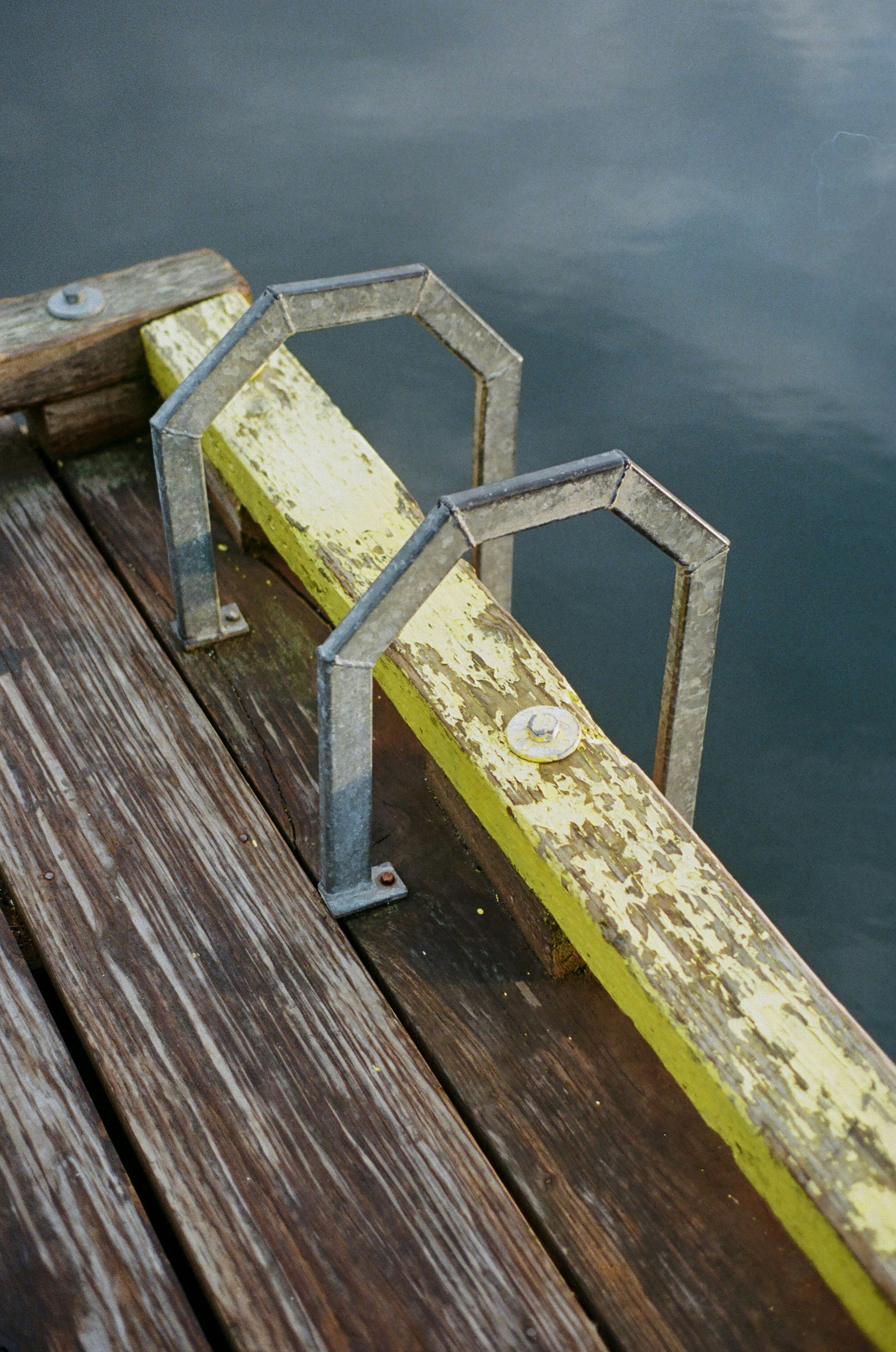 Weathered wooden dock planks stretch toward calm water, framed by hexagonal metal rail supports. This photograph emphasizes texture and peeling paint along the lime-edged railing.