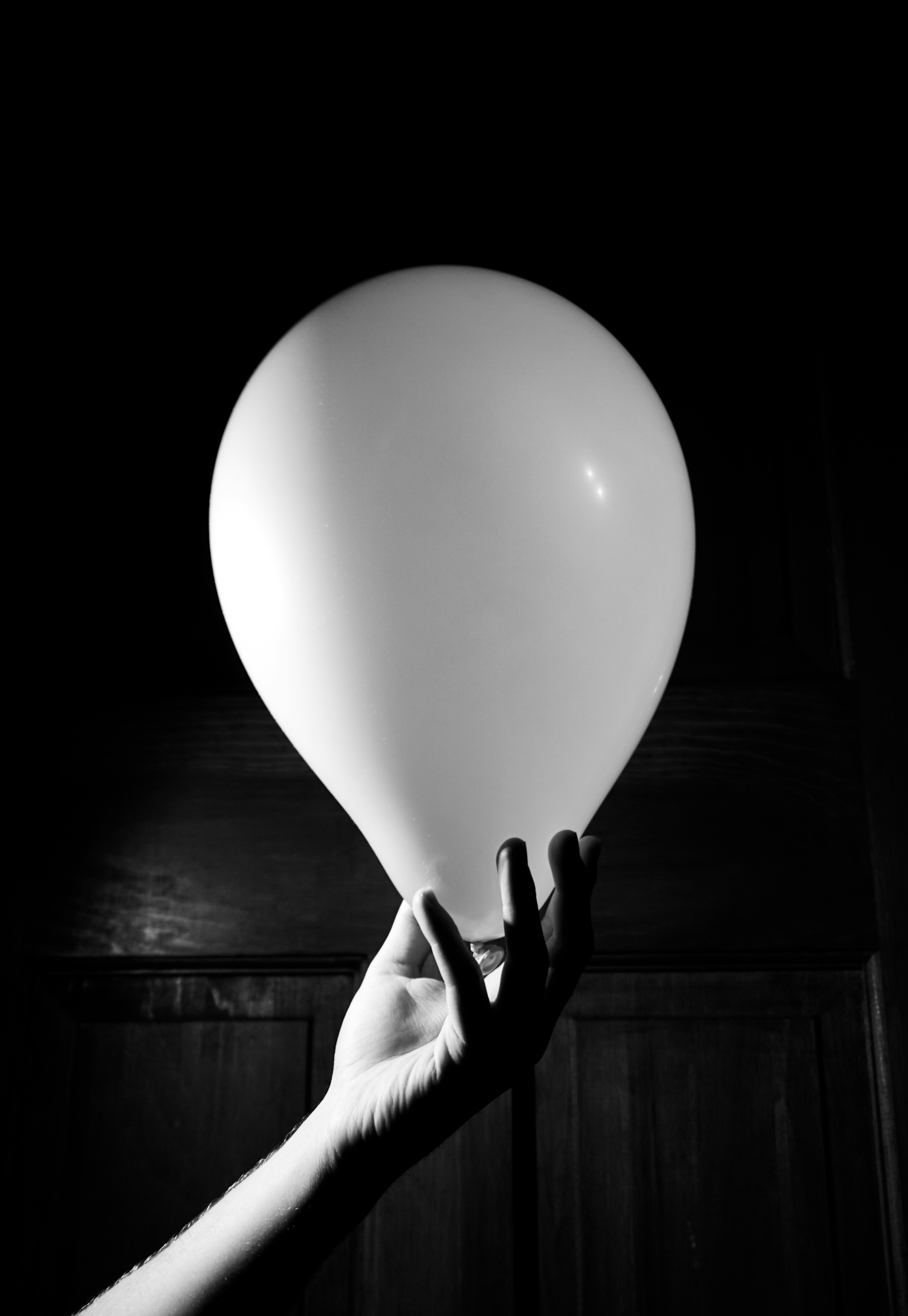 Monochrome Silhouette: Hand and Balloon Against a Dim Wooden Backdrop