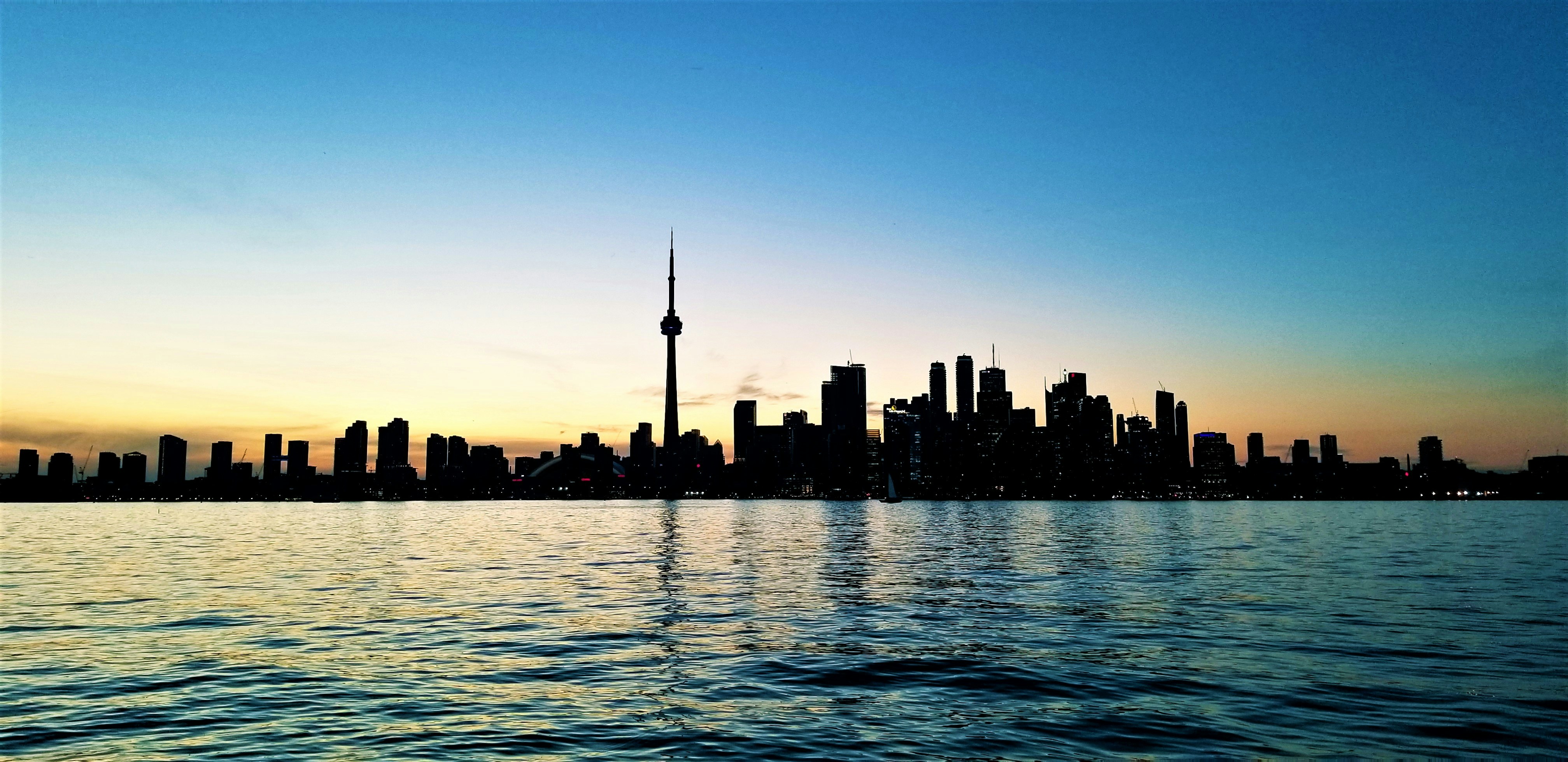City skyline silhouetted against a gradient sunset over calm waters.