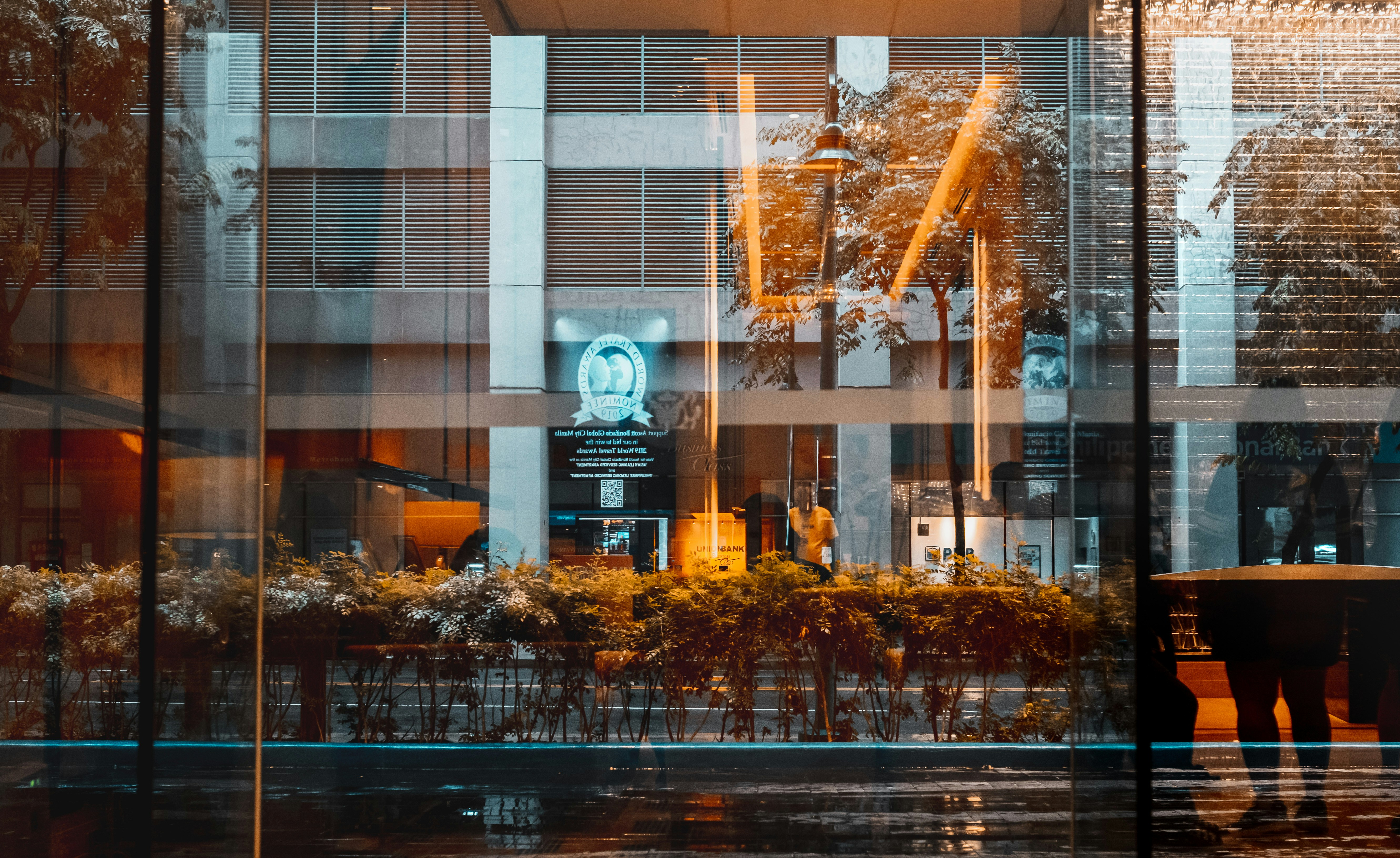 Glass facade reflecting vibrant urban scenery with trees and people, creating a dynamic interplay of nature and architecture.