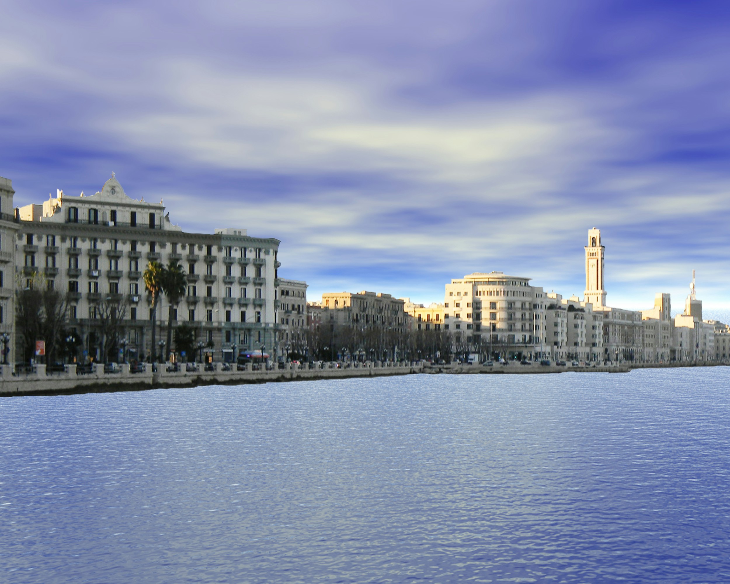 Elegant buildings line a tranquil waterfront under a clear blue sky.