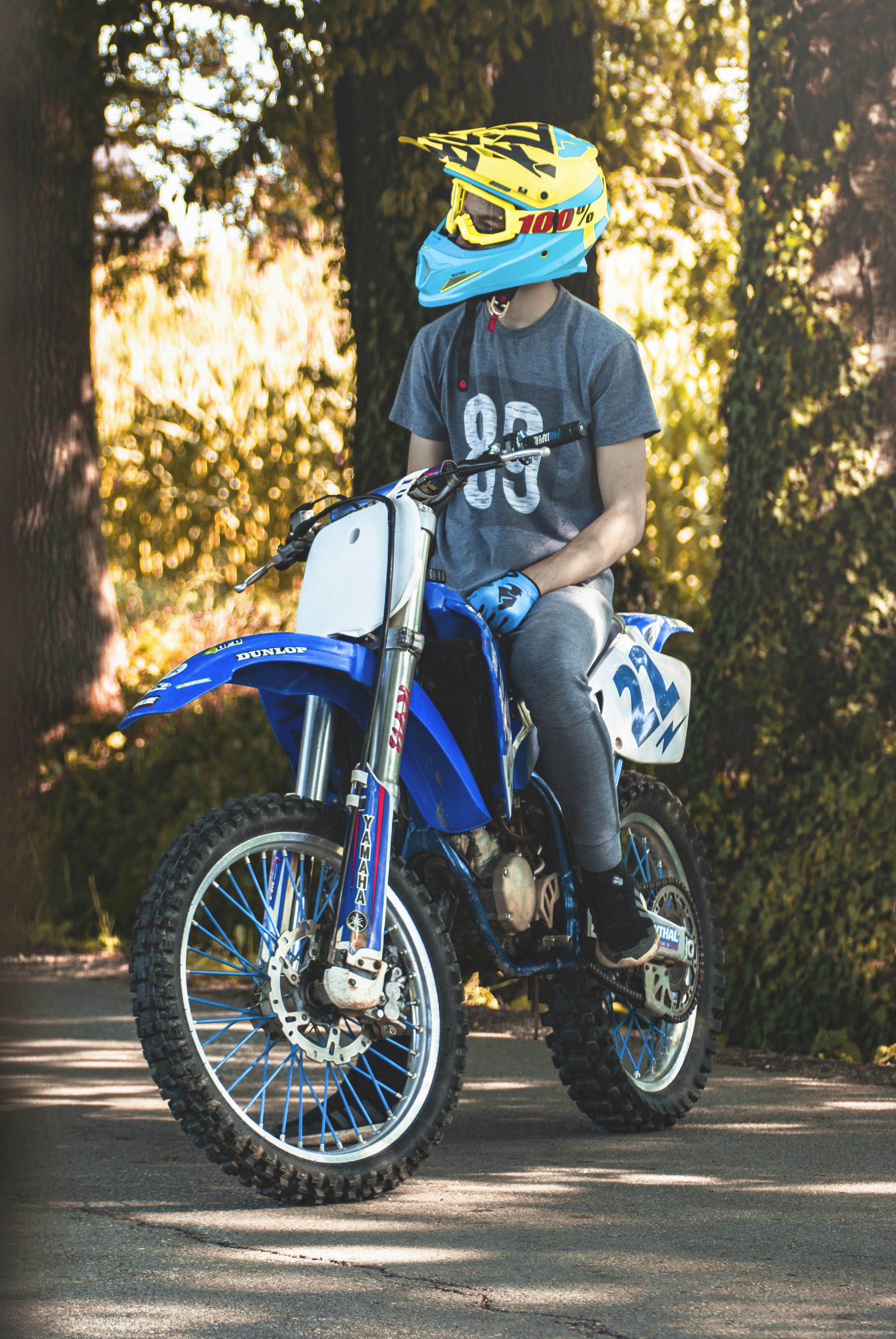 Sunlit Pines: Helmeted Rider Pauses on a Blue Dirt Bike