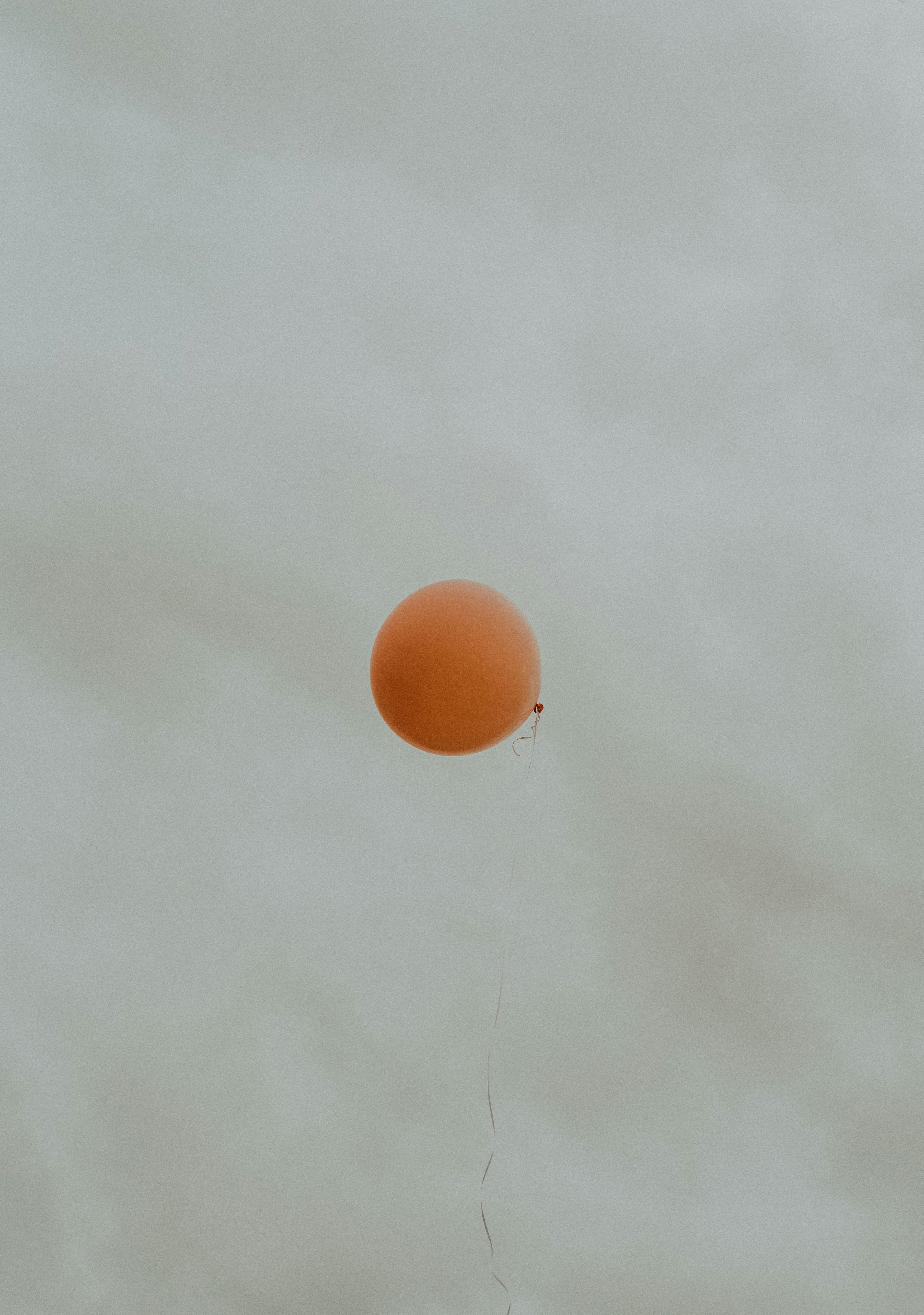 An orange balloon floats against a backdrop of soft, gray clouds, evoking a sense of freedom and whimsy.