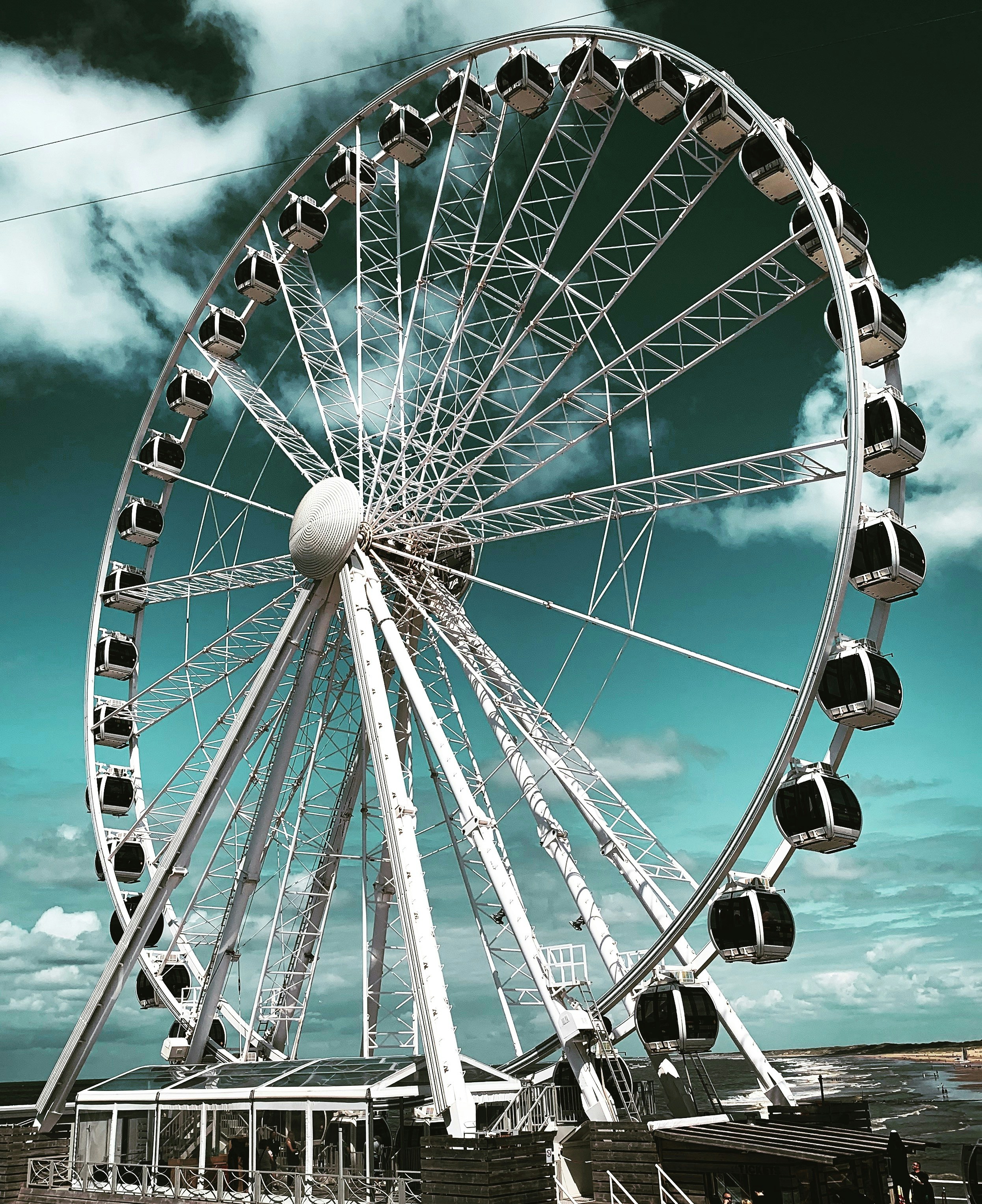 A towering Ferris wheel stands against a vibrant sky, showcasing its intricate structure and suspended cabins. The scene captures the essence of amusement and leisure.