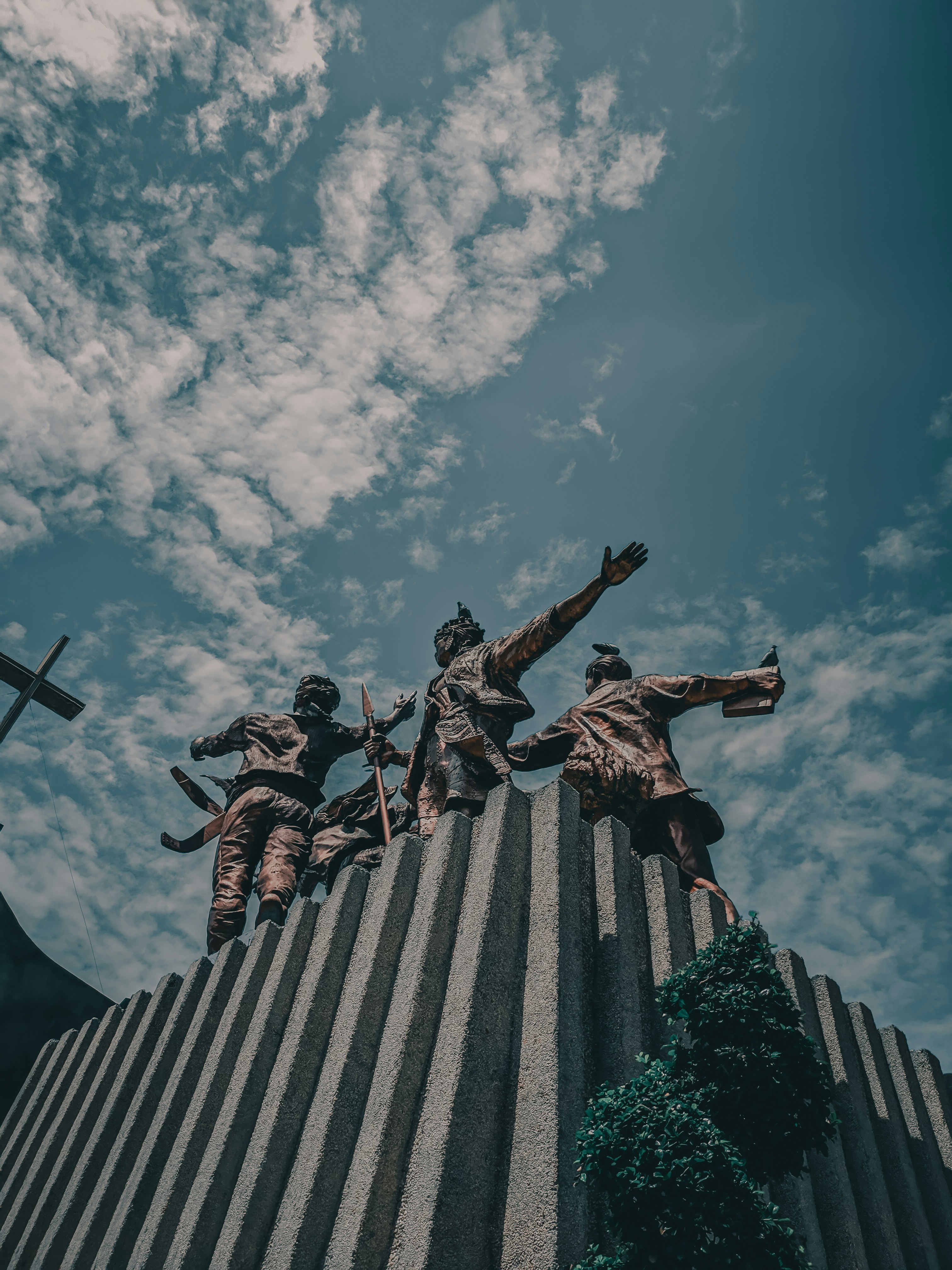 Bronze statues depicting historical figures atop a textured pedestal, set against a dramatic sky. The scene conveys a sense of triumph and remembrance.