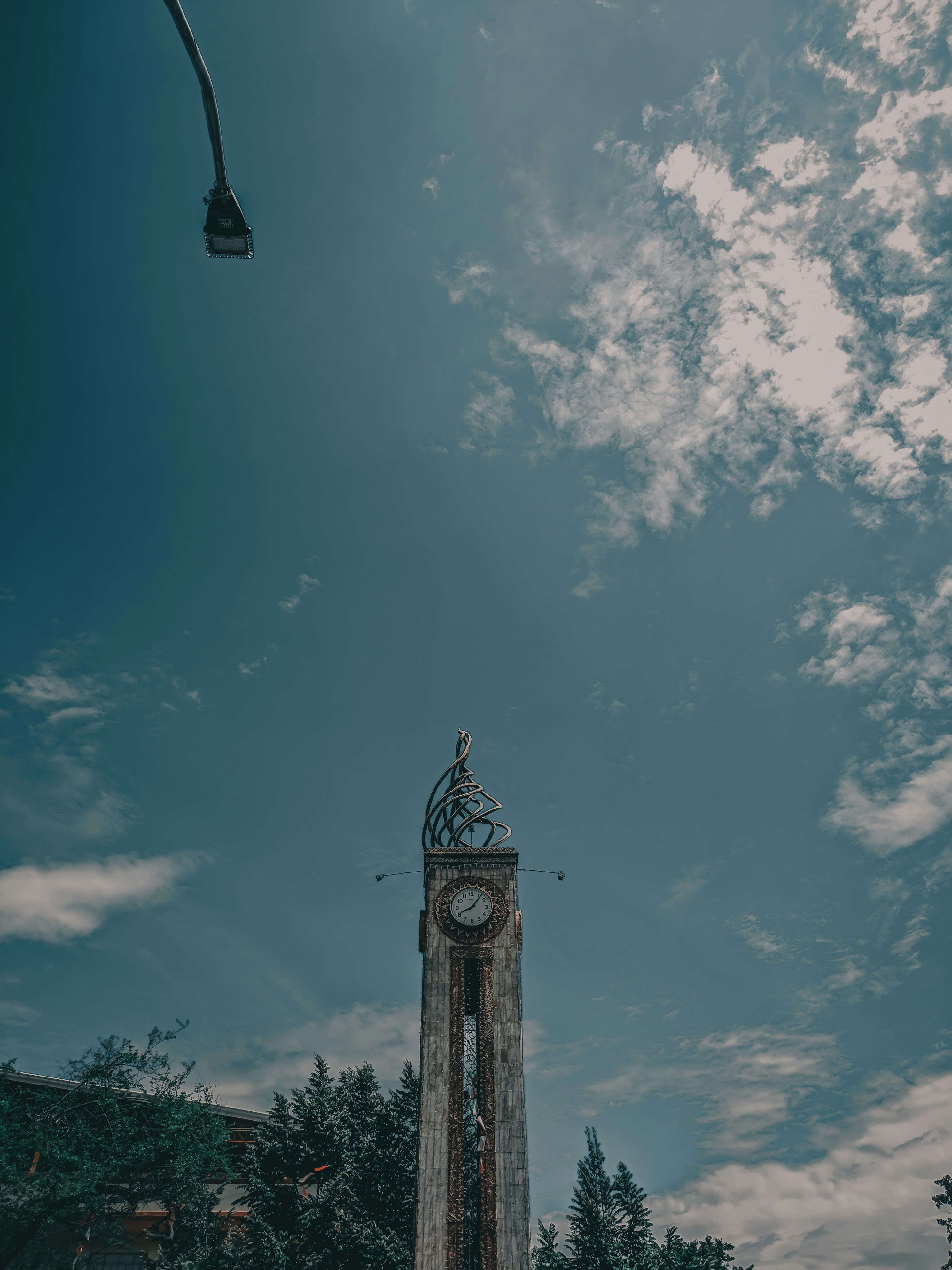 A towering clock structure adorned with intricate designs stands against a backdrop of vibrant blue sky and scattered clouds.