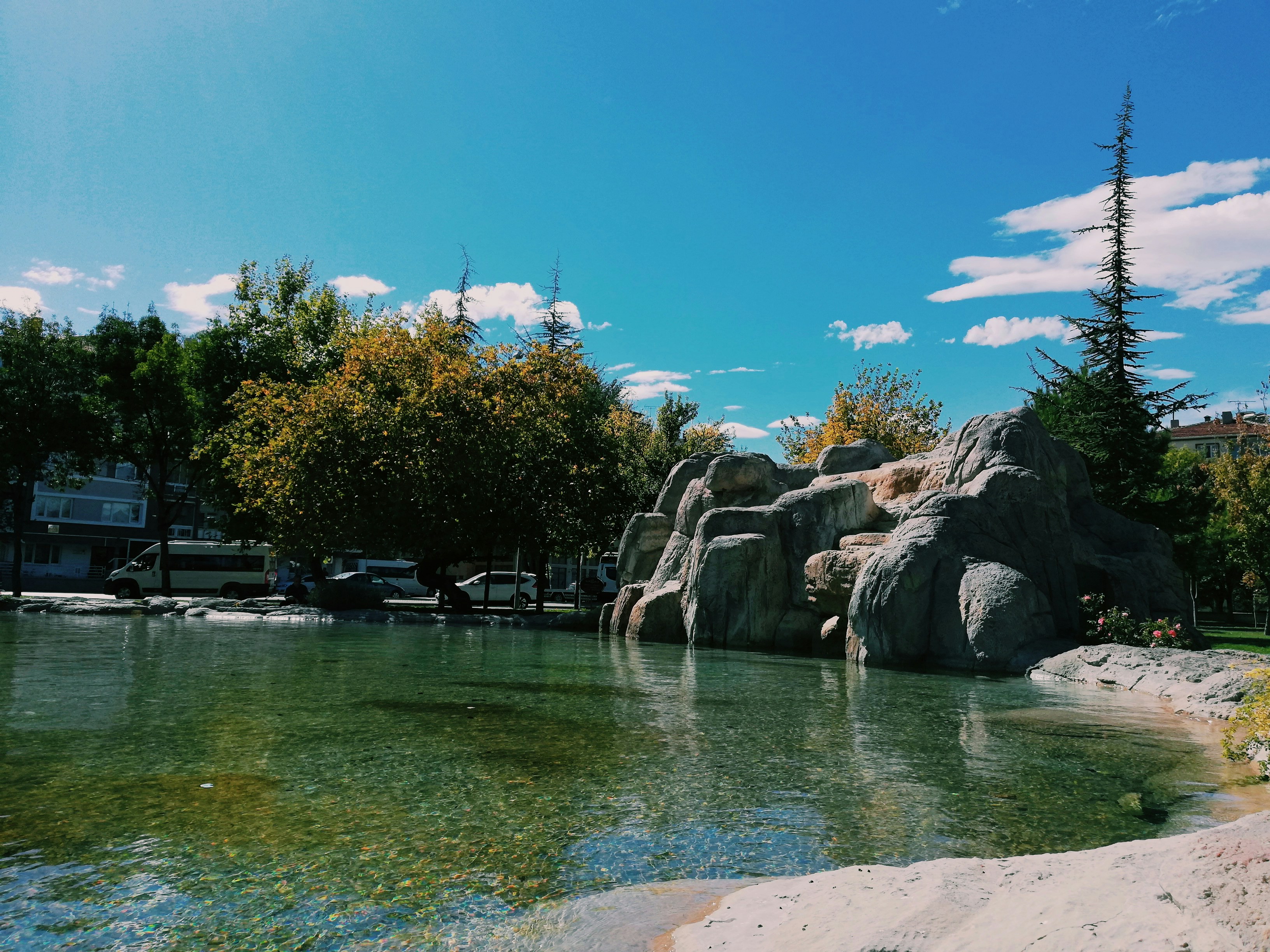 Crystal-clear water reflecting vibrant autumn foliage and rocky formations in a tranquil park setting.