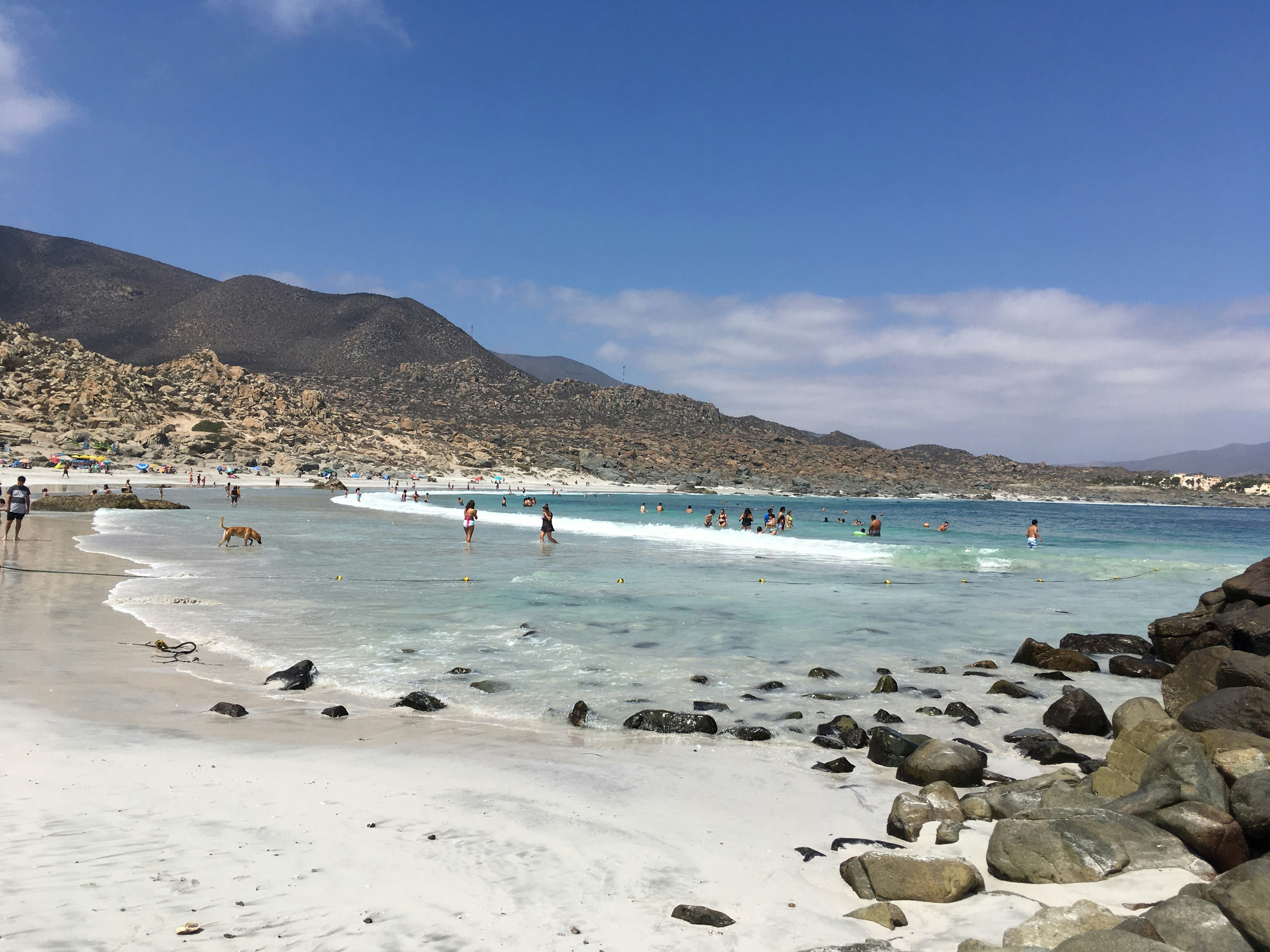 Sandy beach with gentle waves meeting rocky shore under a bright blue sky.