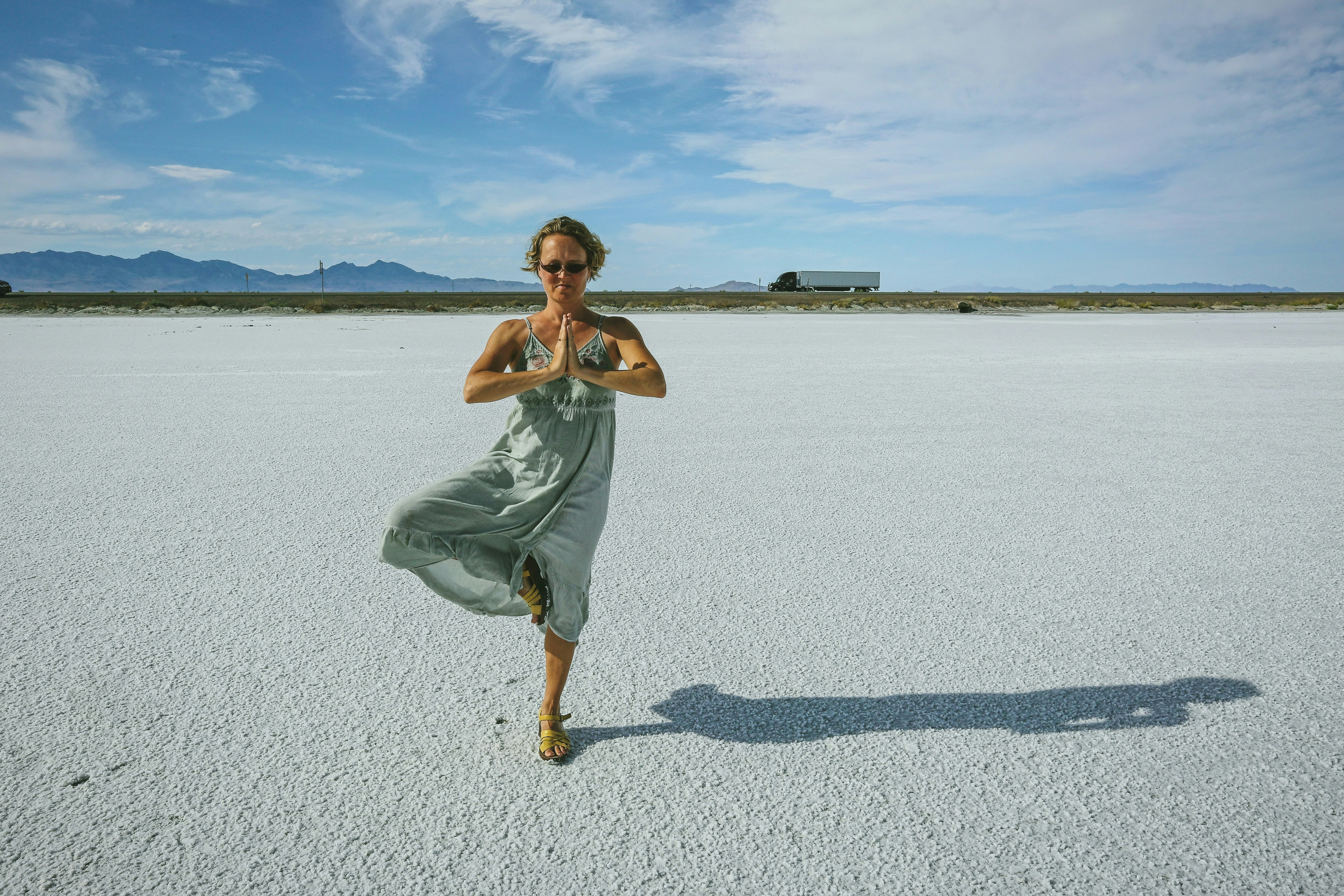 Person in a yoga pose on expansive white salt flats under a bright blue sky.