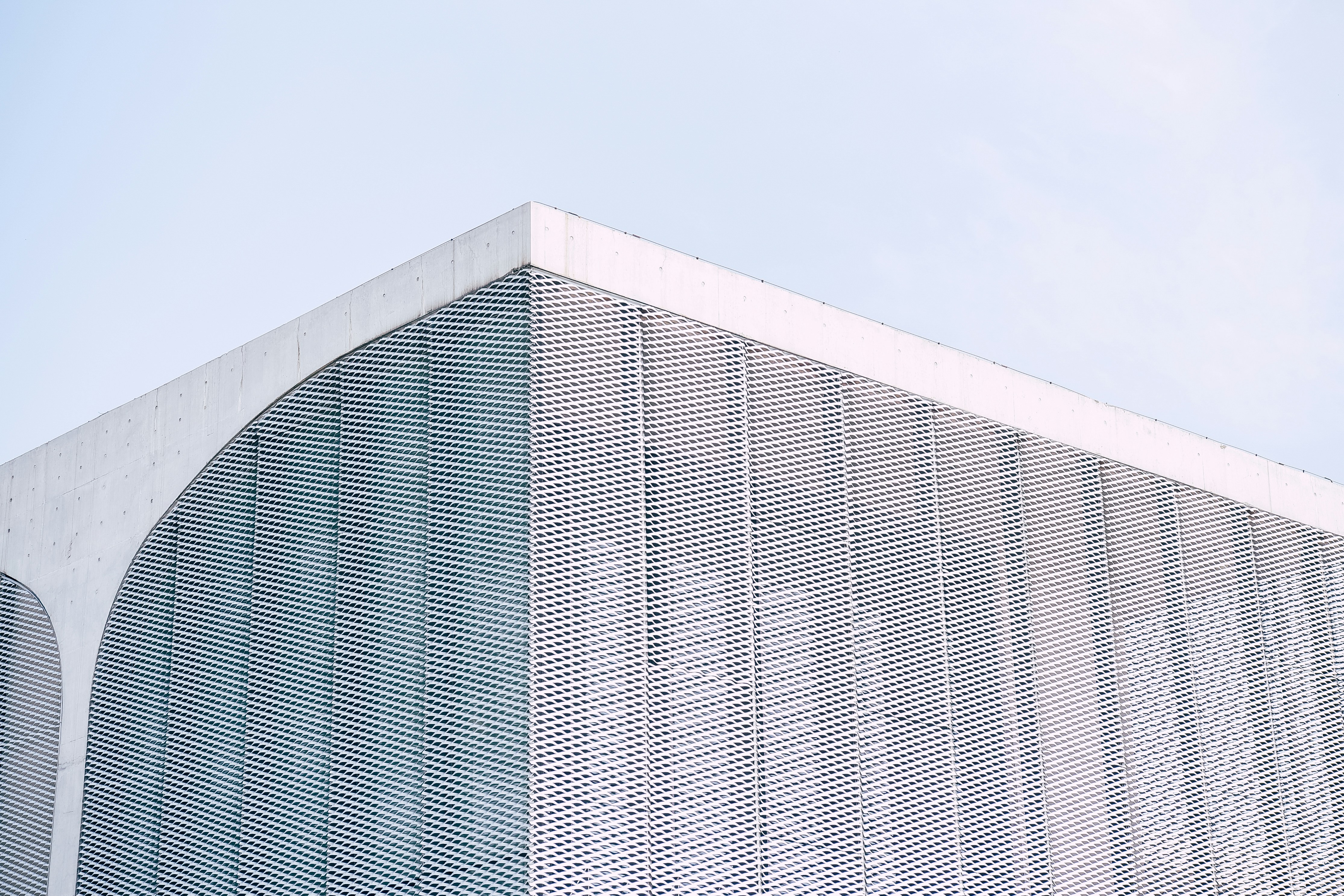 Modern architectural facade with vertical lines and soft curves under a pale blue sky.