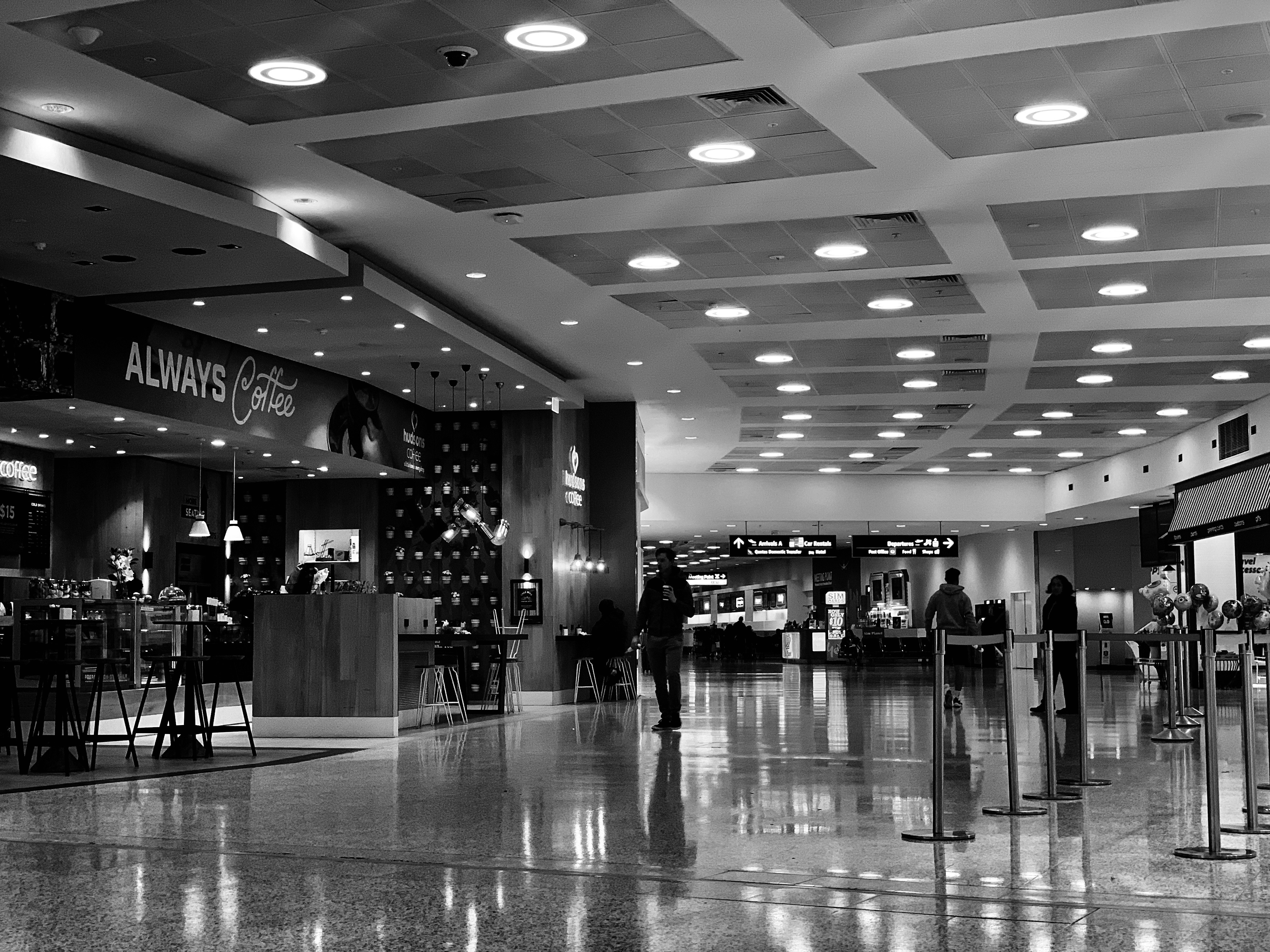 Coffee shop in an airport terminal with patrons waiting in line and soft lighting illuminating the space.