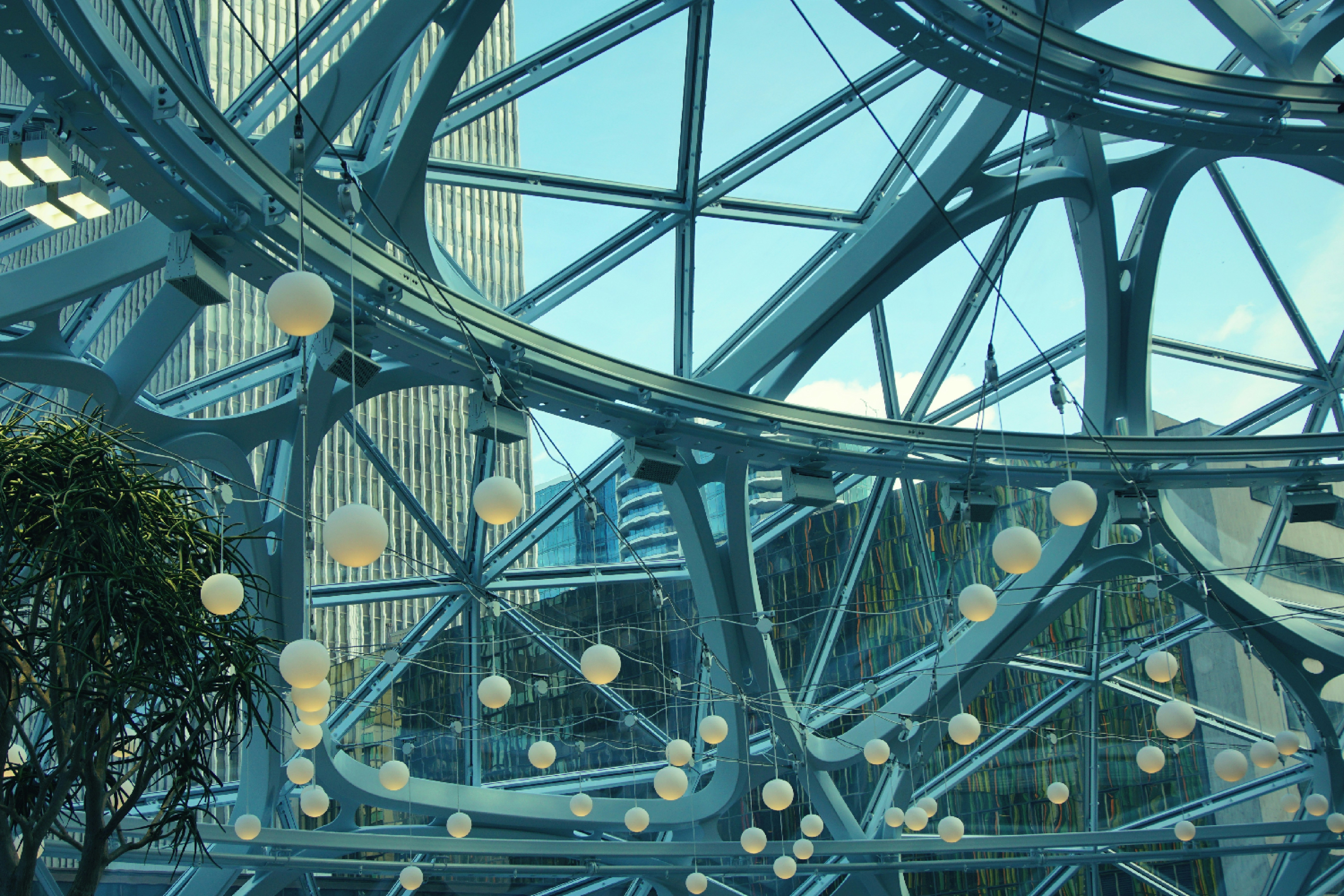 Intricate geometric framework adorned with hanging lights, set against a backdrop of modern skyscrapers.