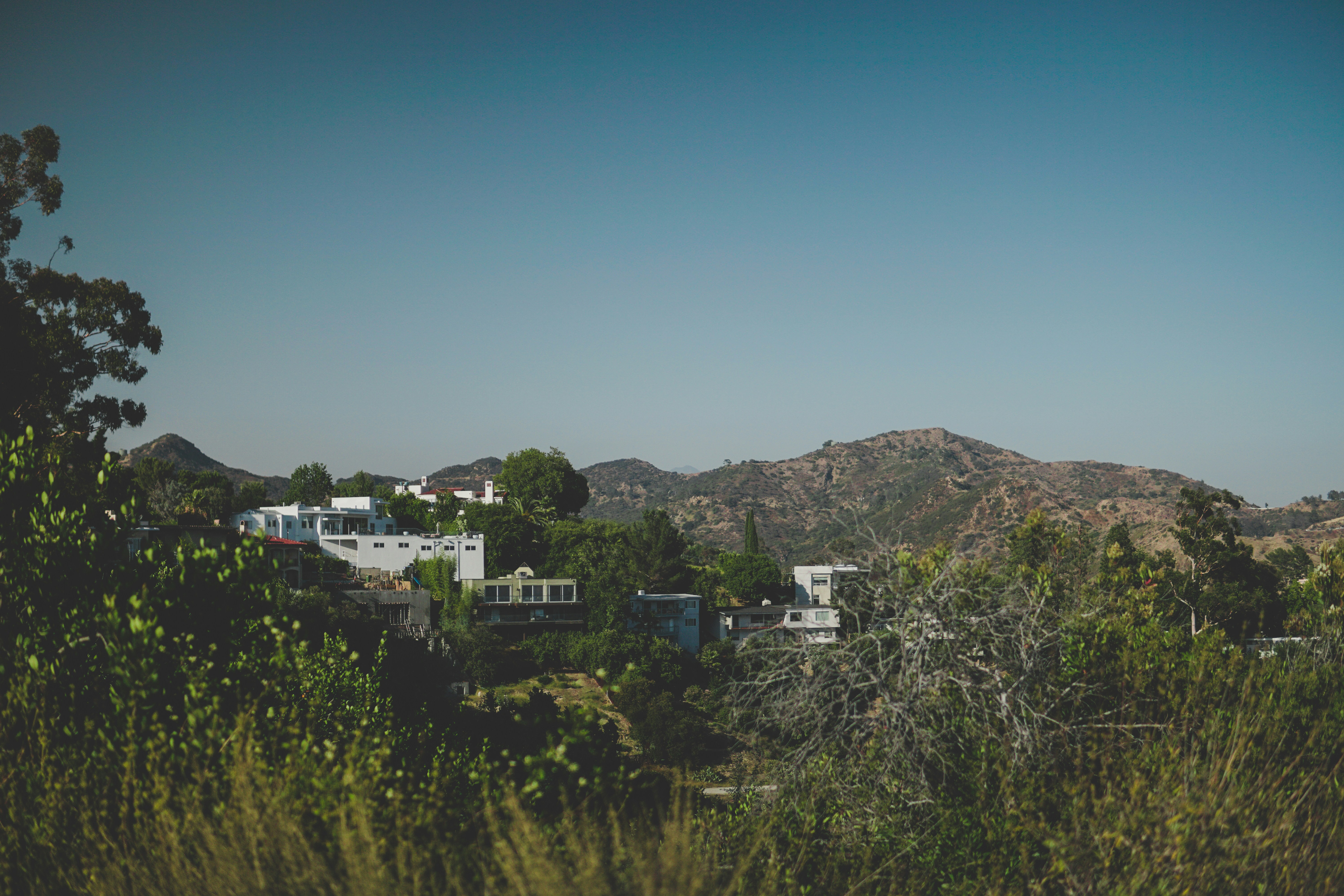 Hillside homes nestled among lush greenery, framed by distant mountains under a clear blue sky.