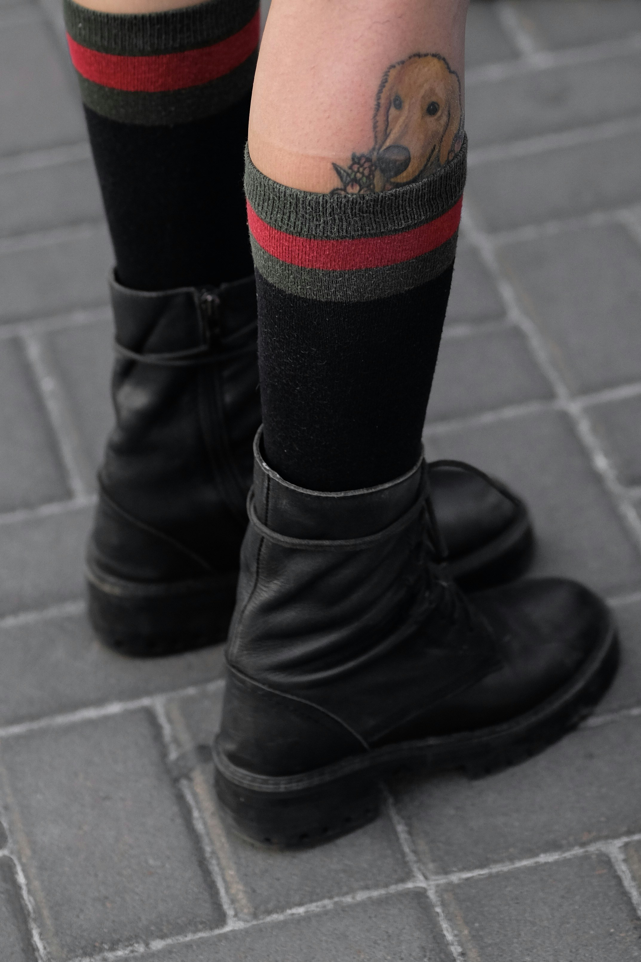 Close-up of black combat boots paired with striped socks, revealing a playful tattoo of a golden retriever on the calf.