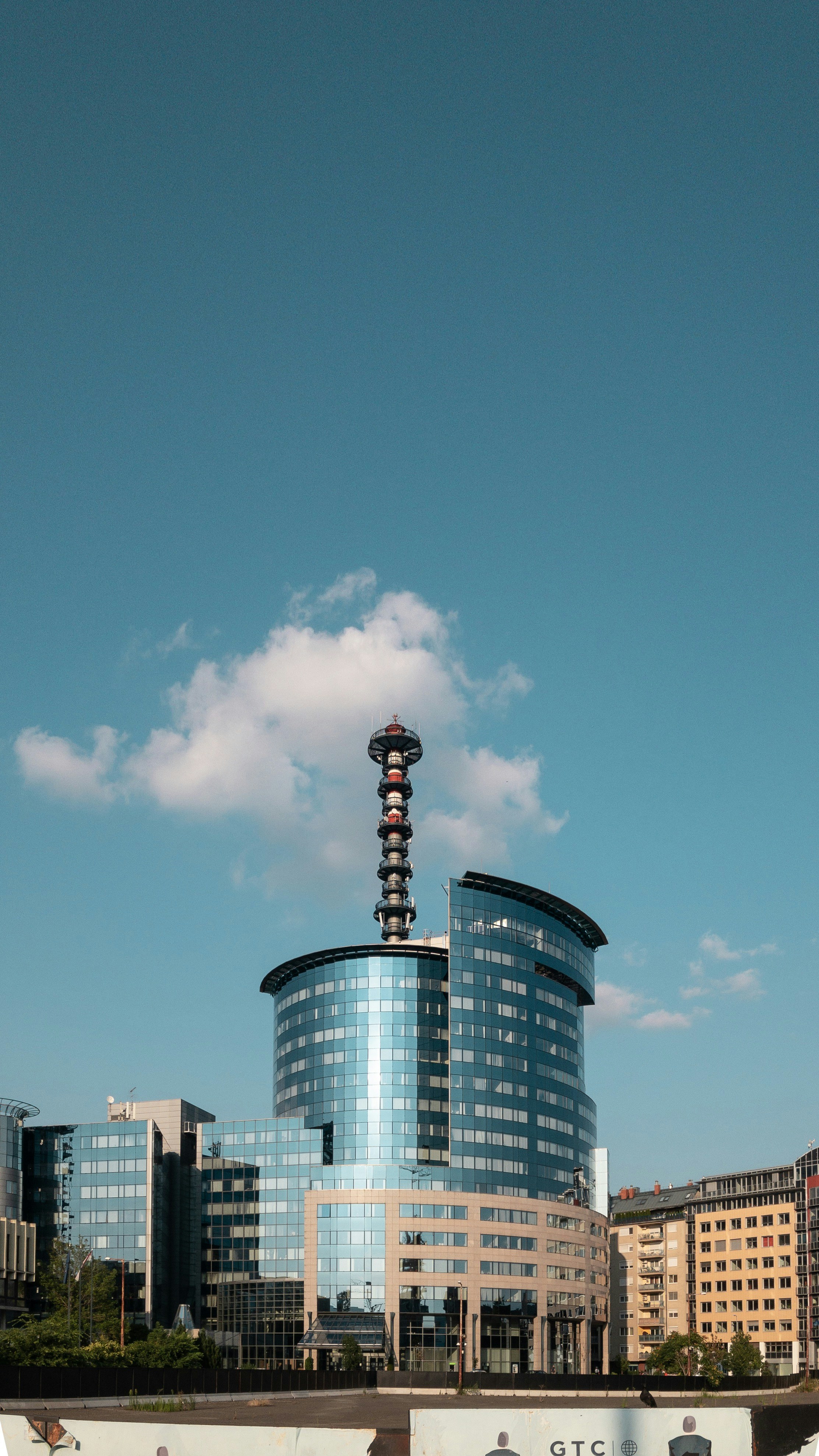 Sleek glass building with a prominent communication tower against a clear blue sky, showcasing contemporary architecture.