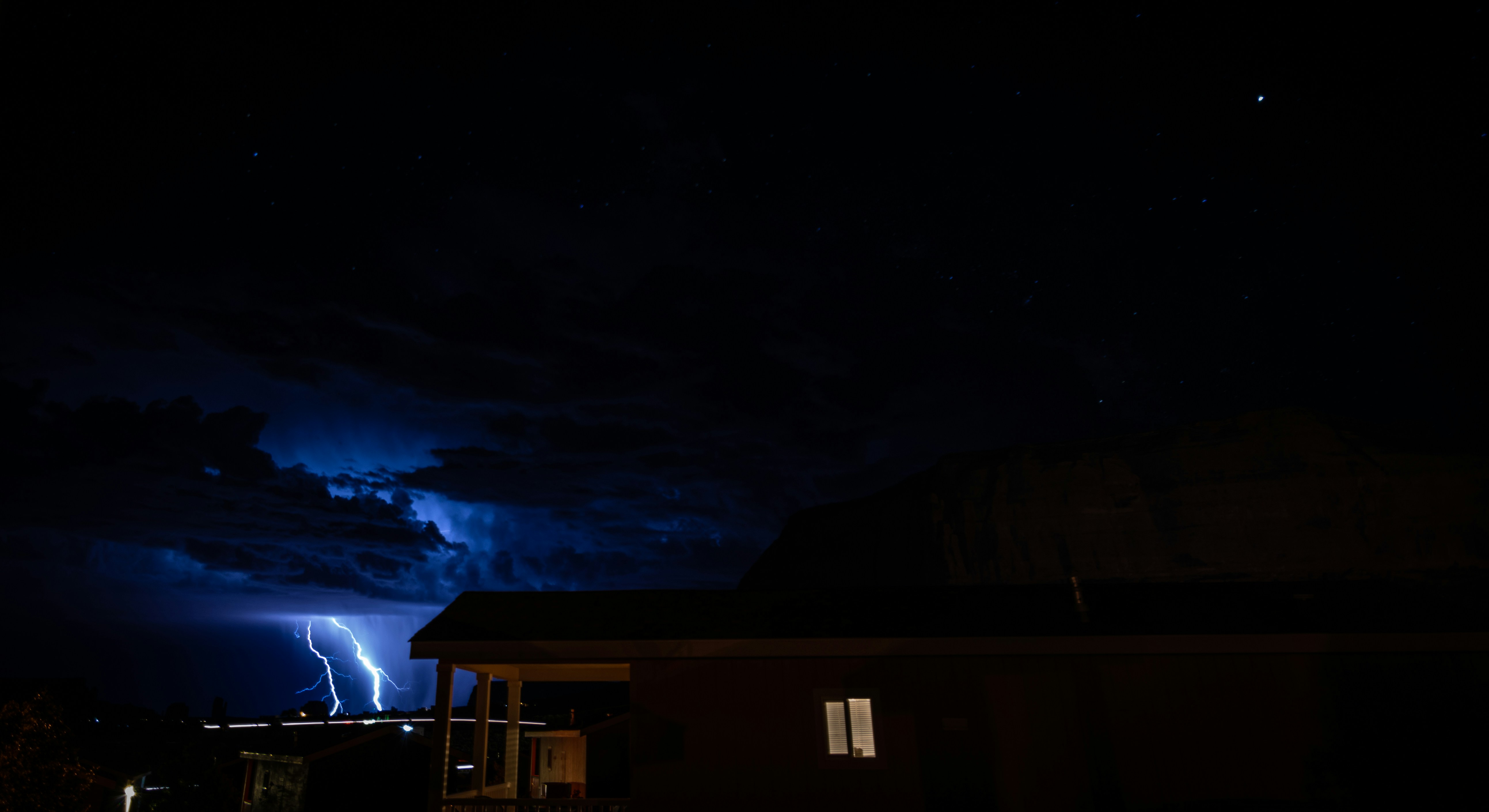 Lightning illuminates a dark sky, contrasting against the silhouette of a building below. The scene captures the raw power of nature during a storm.