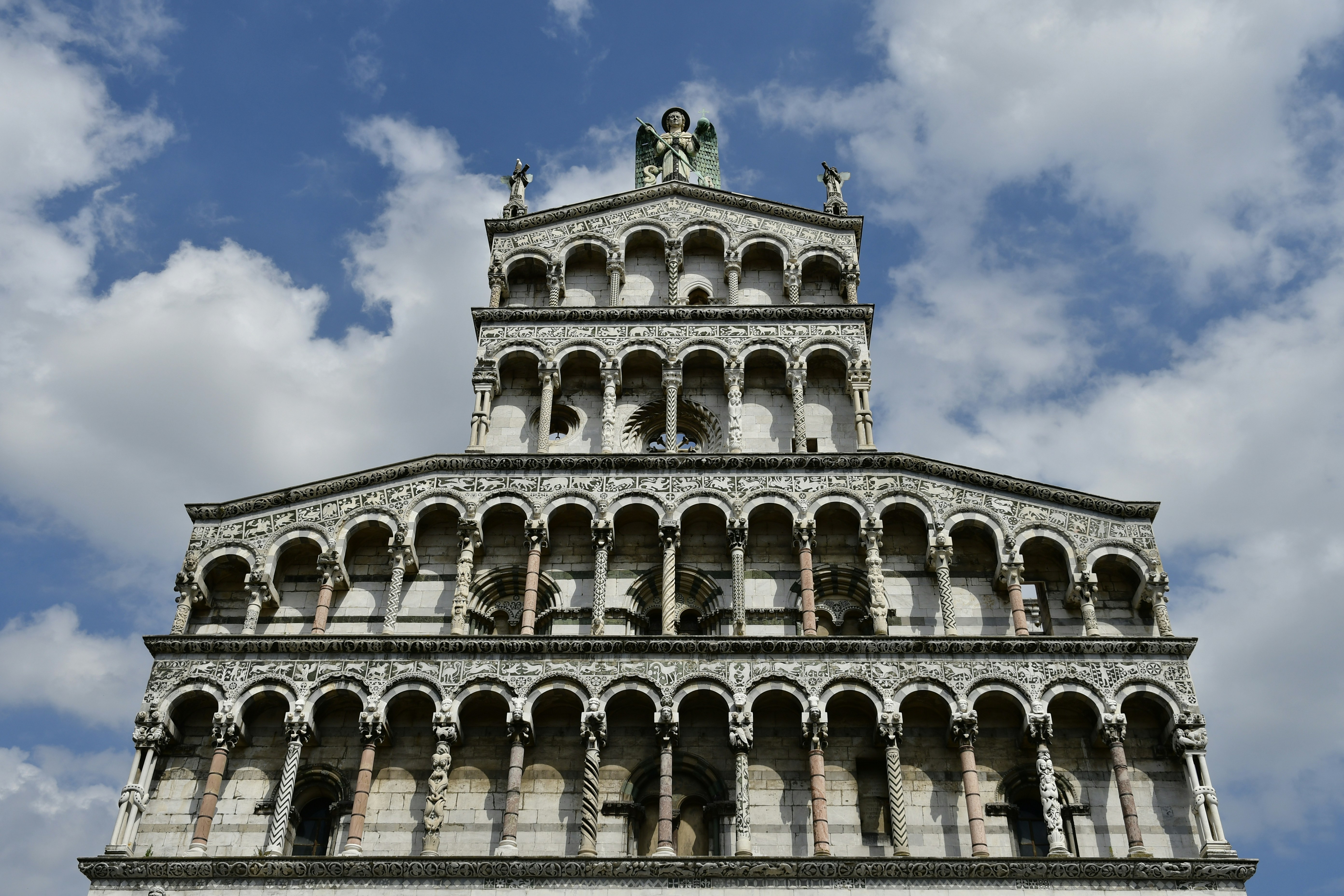 Intricate facade of a historic church in Lucca against a backdrop of fluffy clouds.