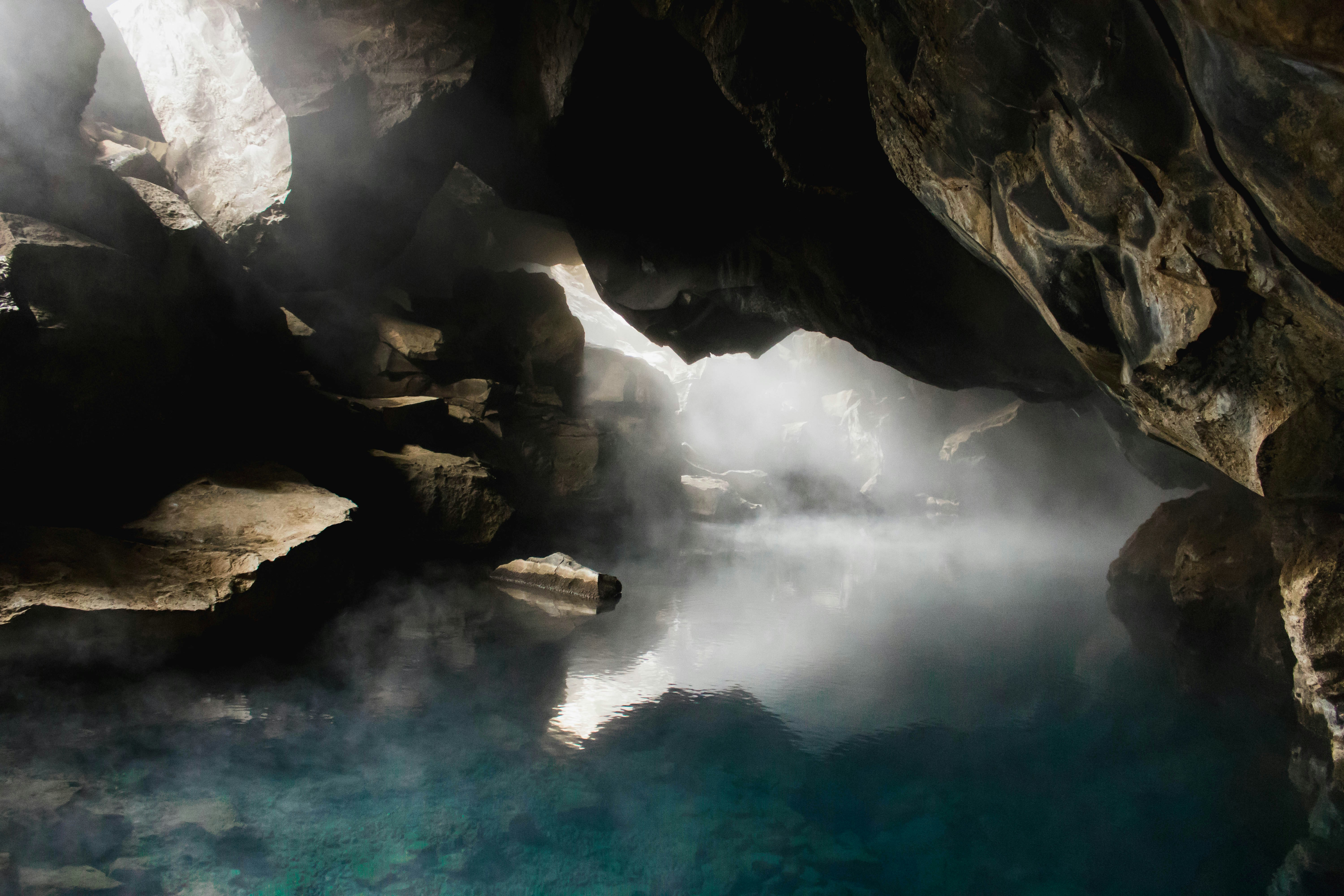 Sunlight streams into a tranquil cave, illuminating the still, reflective water below.