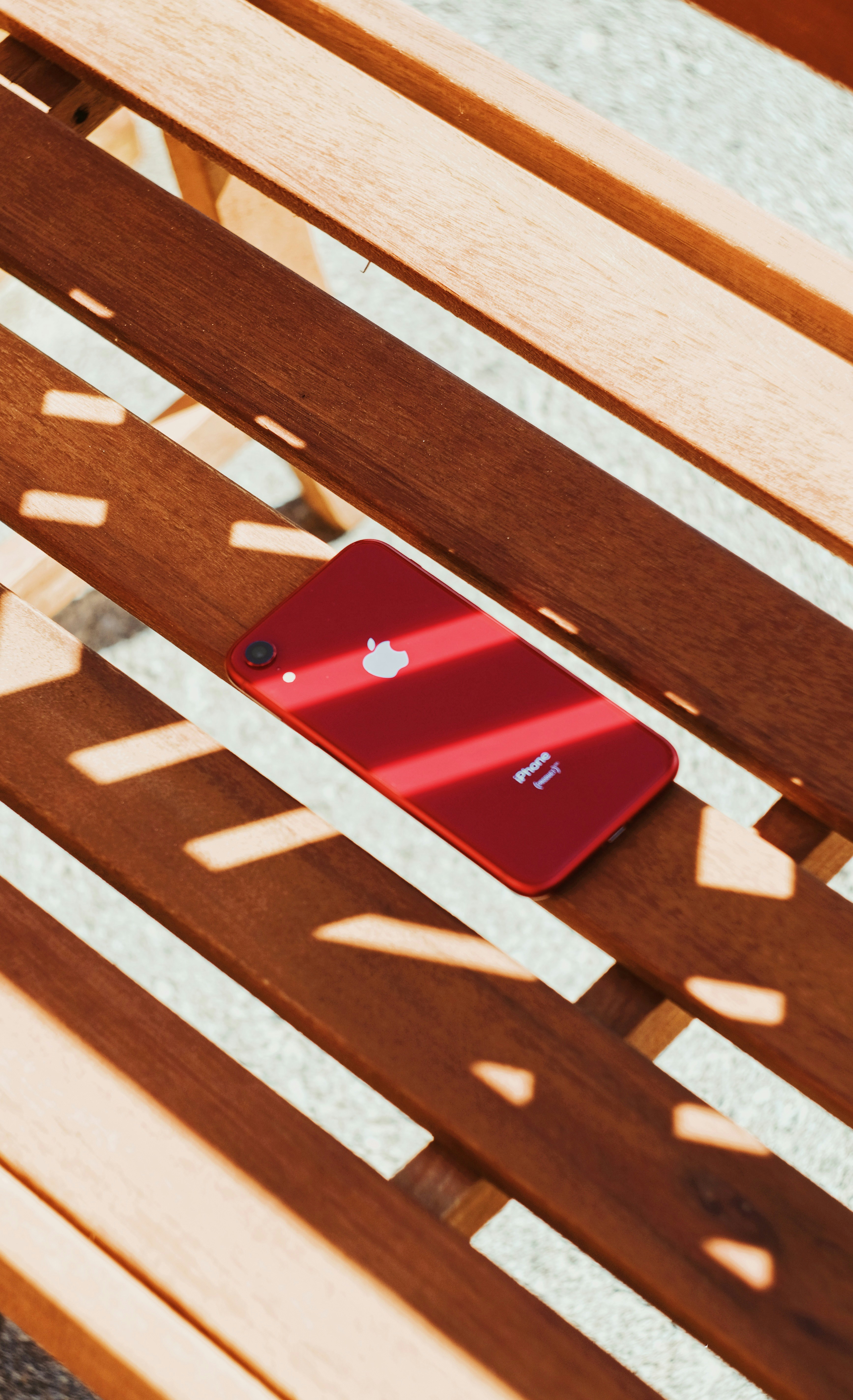 Red Apple iPhone Slotted Between Wooden Slats in Sunlit Court