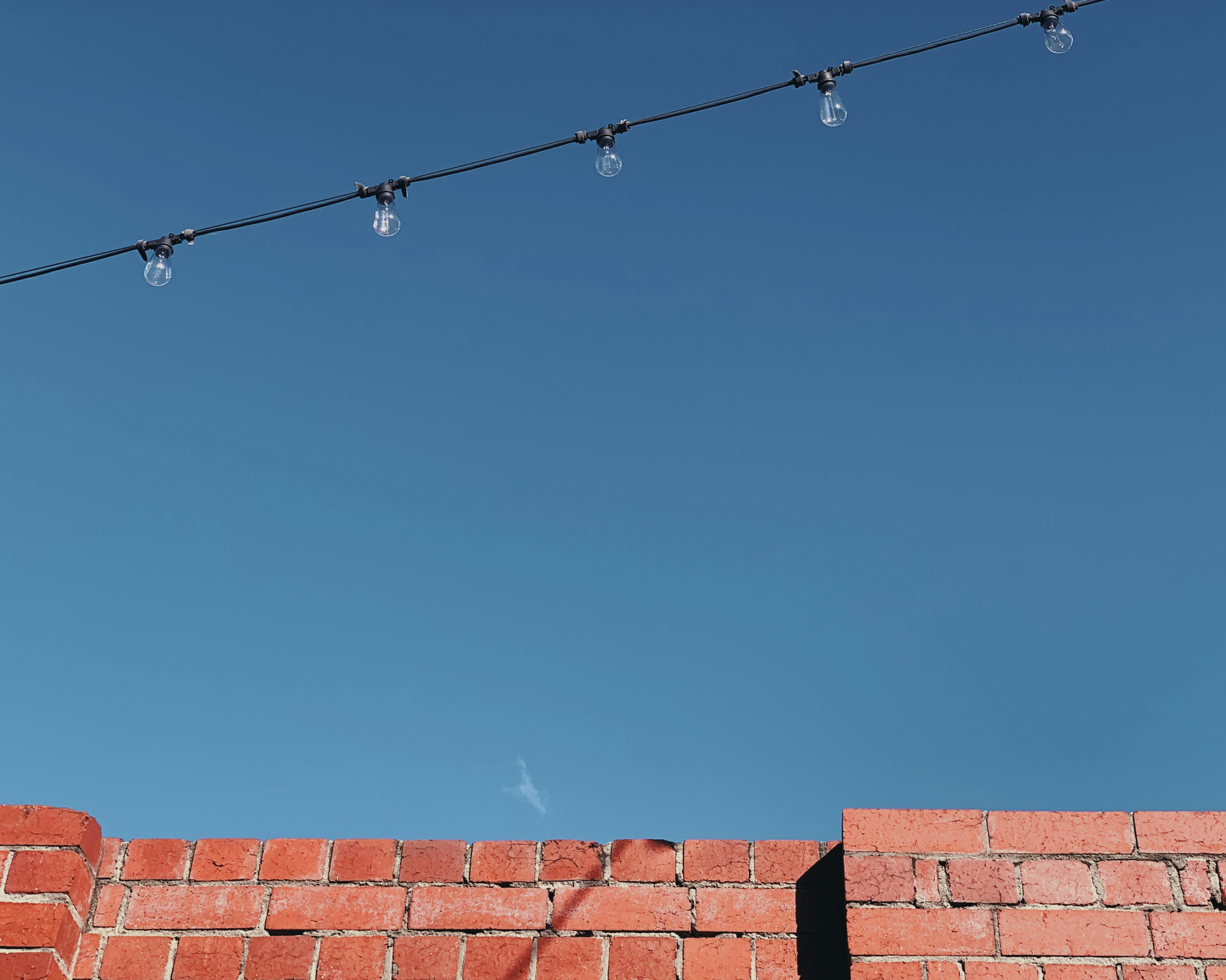 Azure Sky Over a Red Brick Wall with a Row of Bulbs