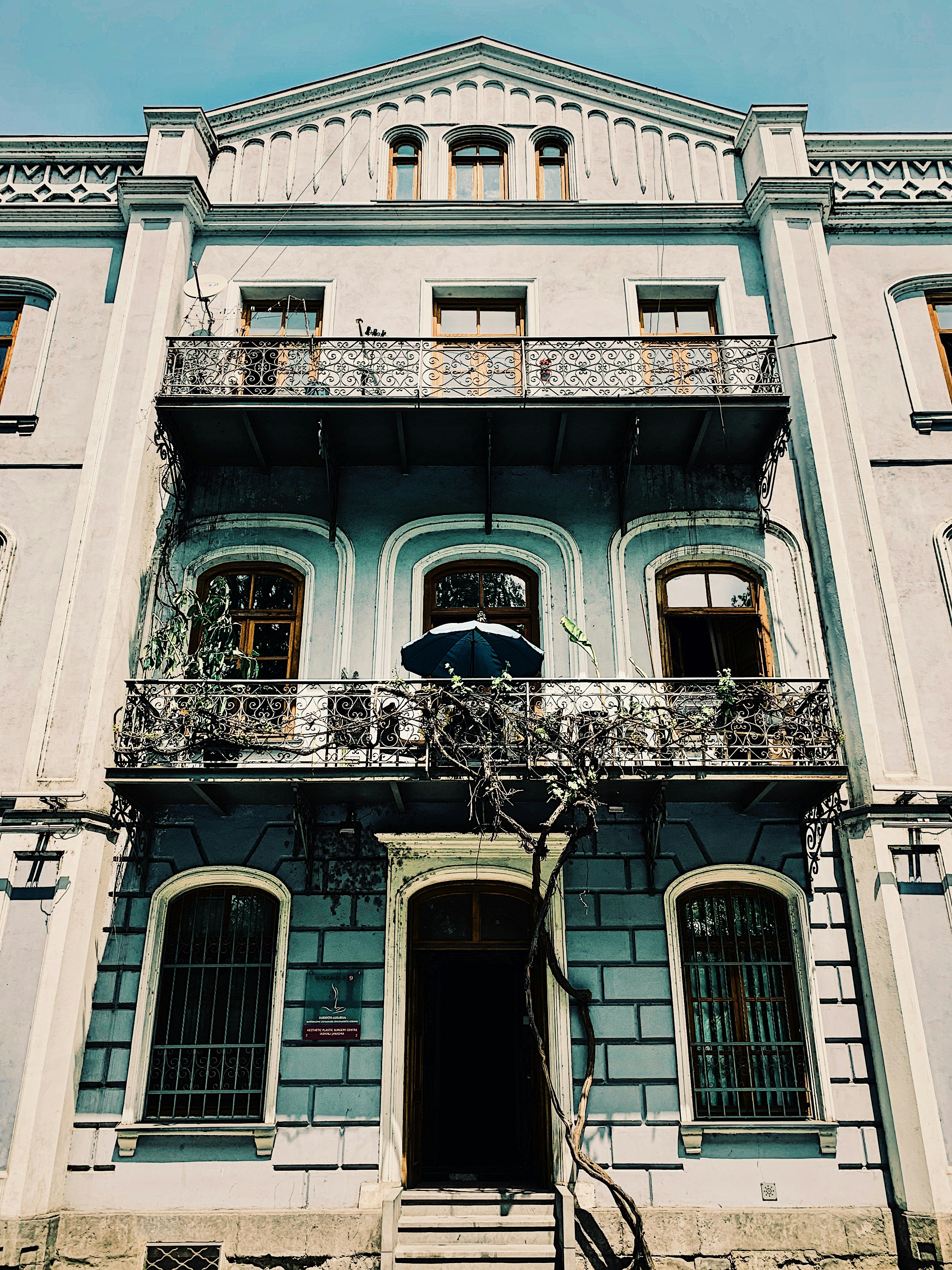 A vintage building with intricate balconies, adorned with creeping vines and an umbrella, showcasing architectural elegance and decay.
