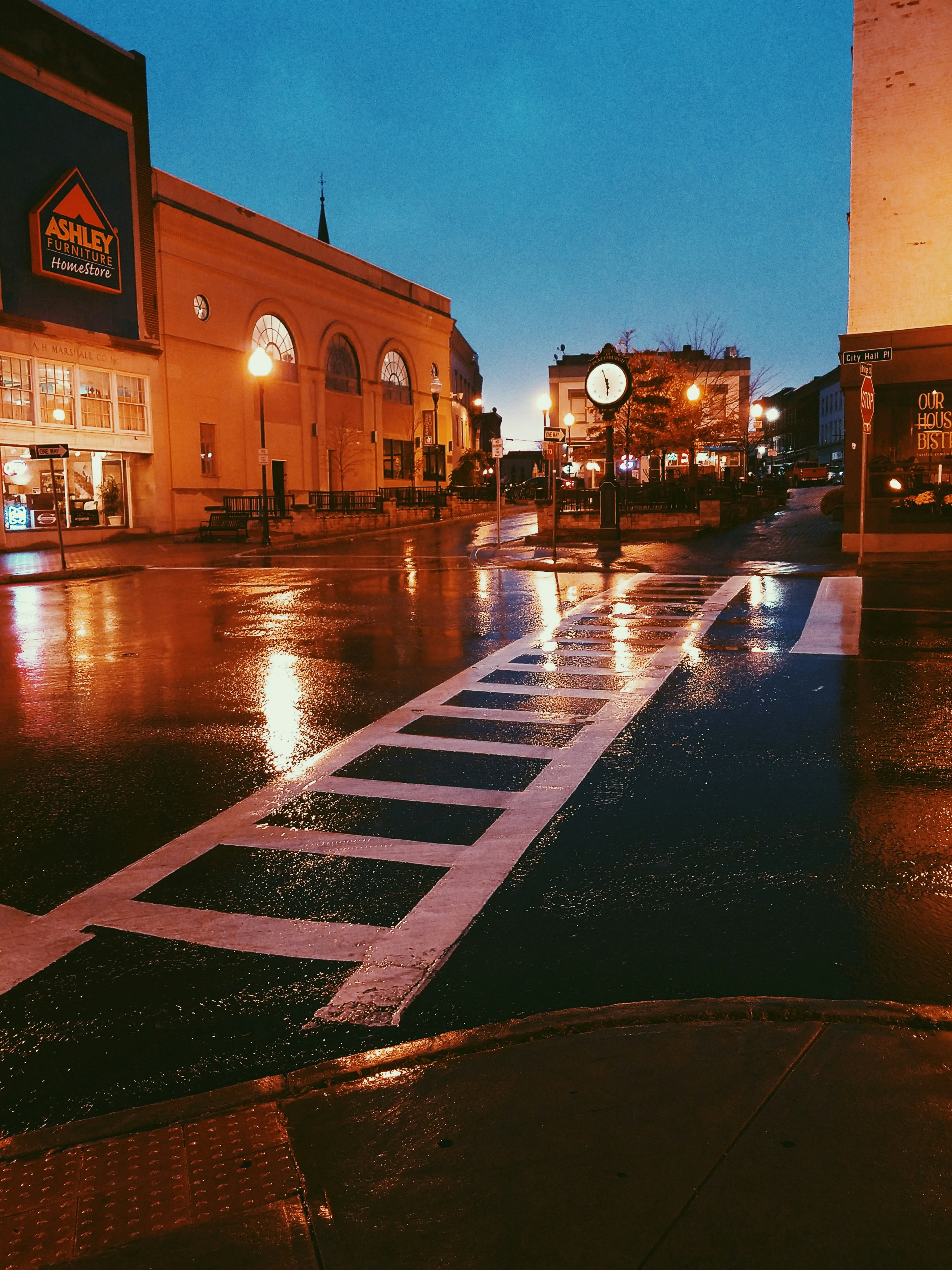 Wet crosswalk reflecting streetlights in a quiet urban setting at dusk.