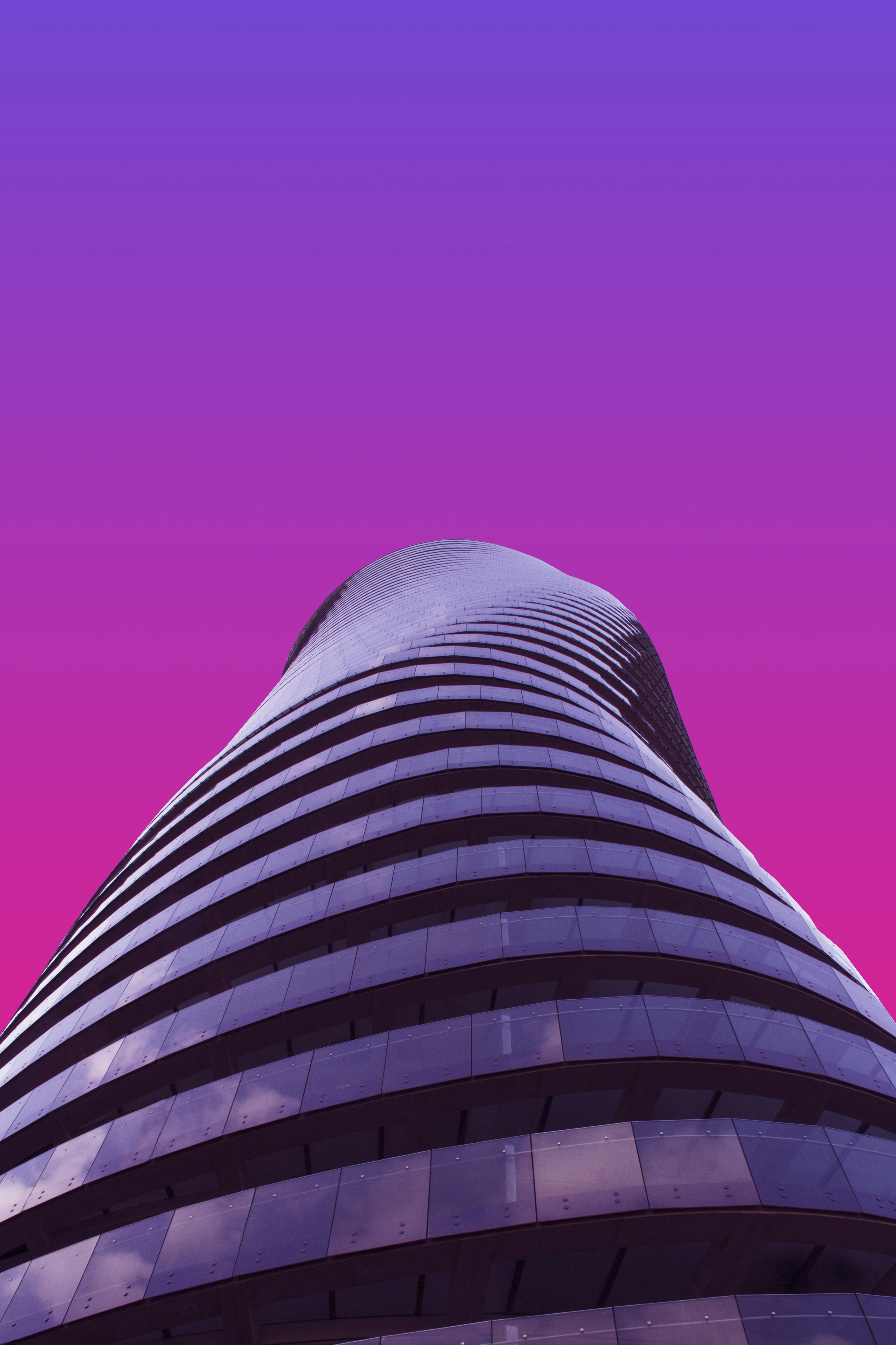A sleek, spiraling skyscraper stretches upward against a vibrant gradient sky, showcasing its contemporary architectural design.