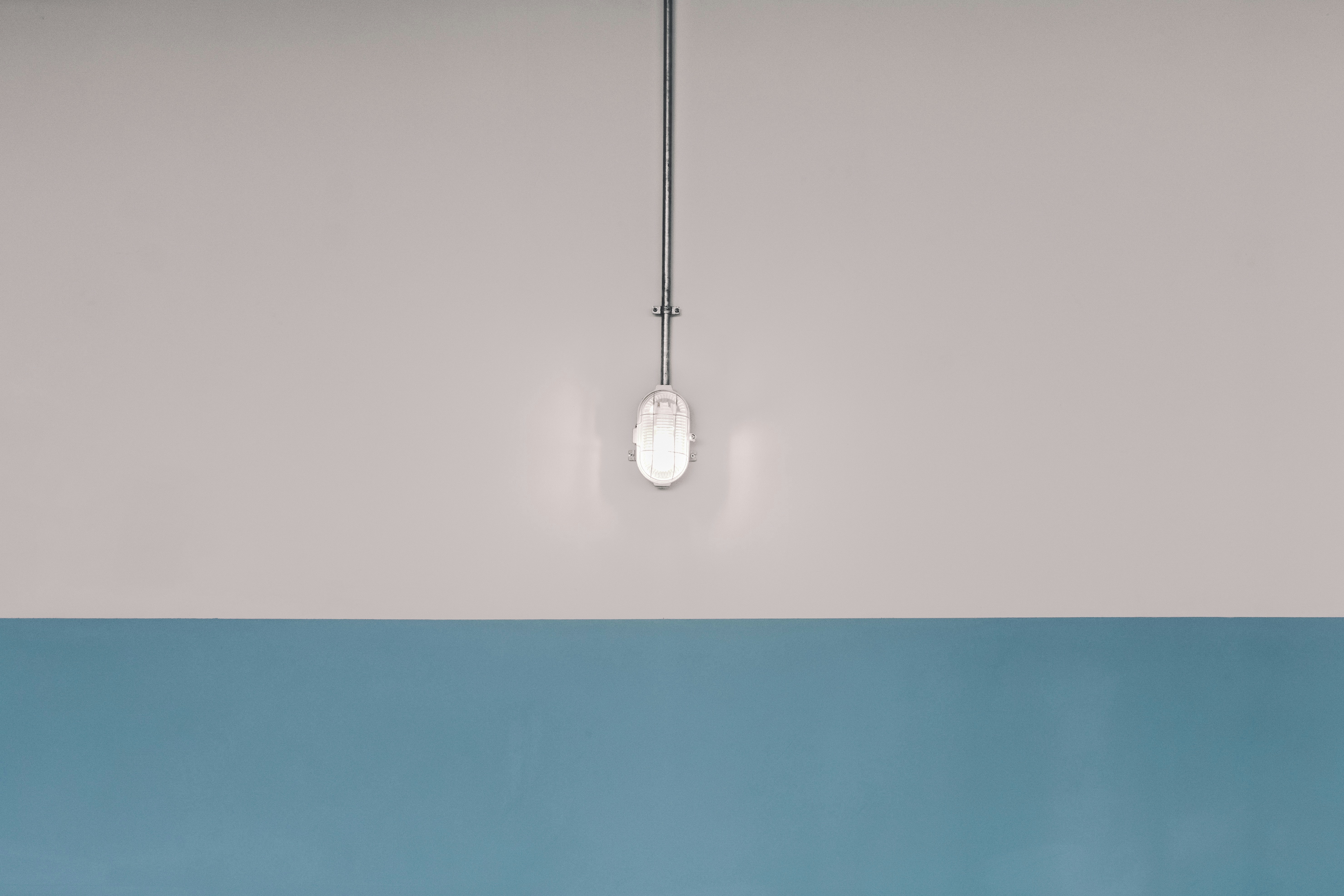 A single pendant light hangs from a ceiling above a divided wall, featuring a soft gray upper section and a calming blue lower section.