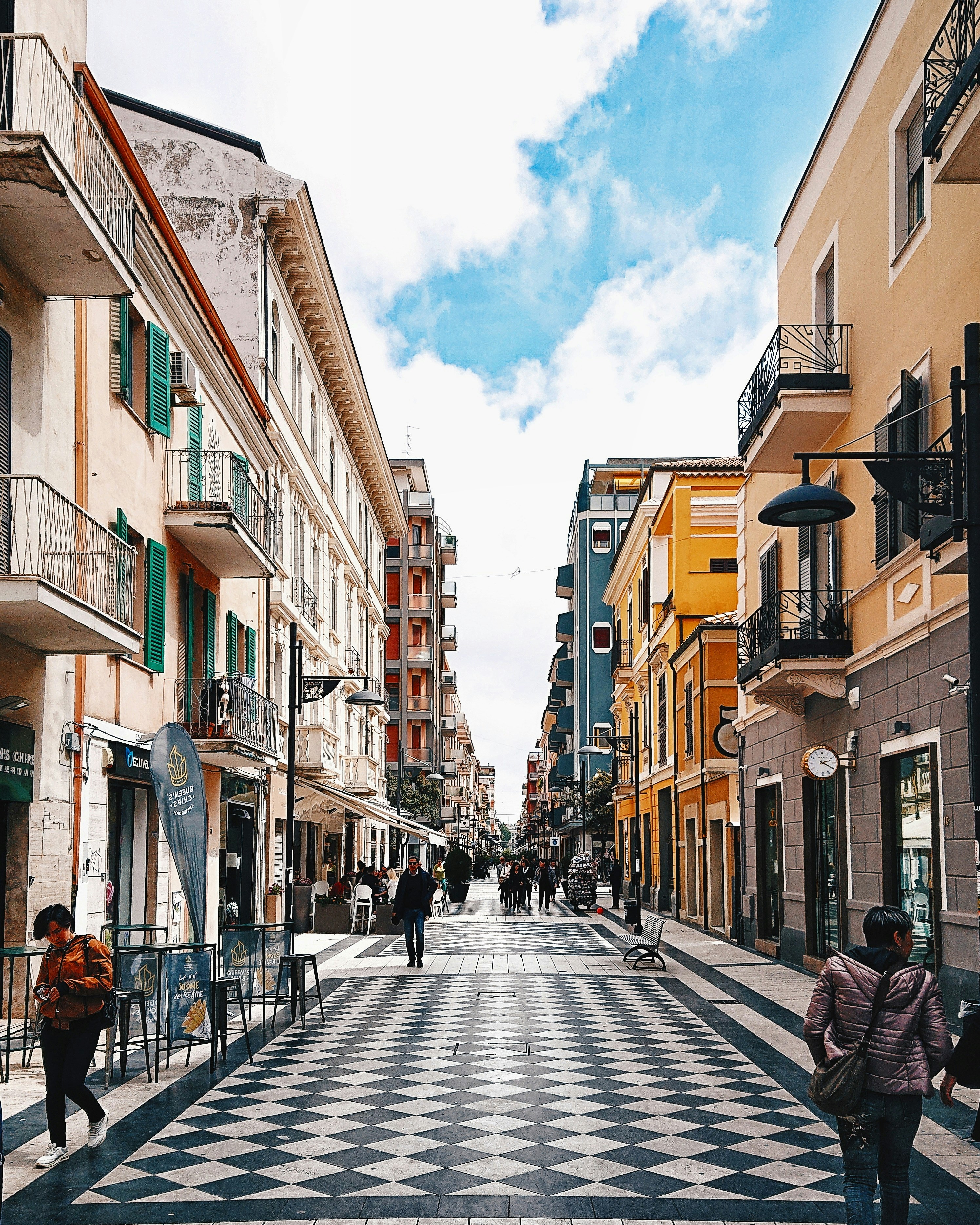 Pedestrian street lined with colorful buildings under a bright blue sky.