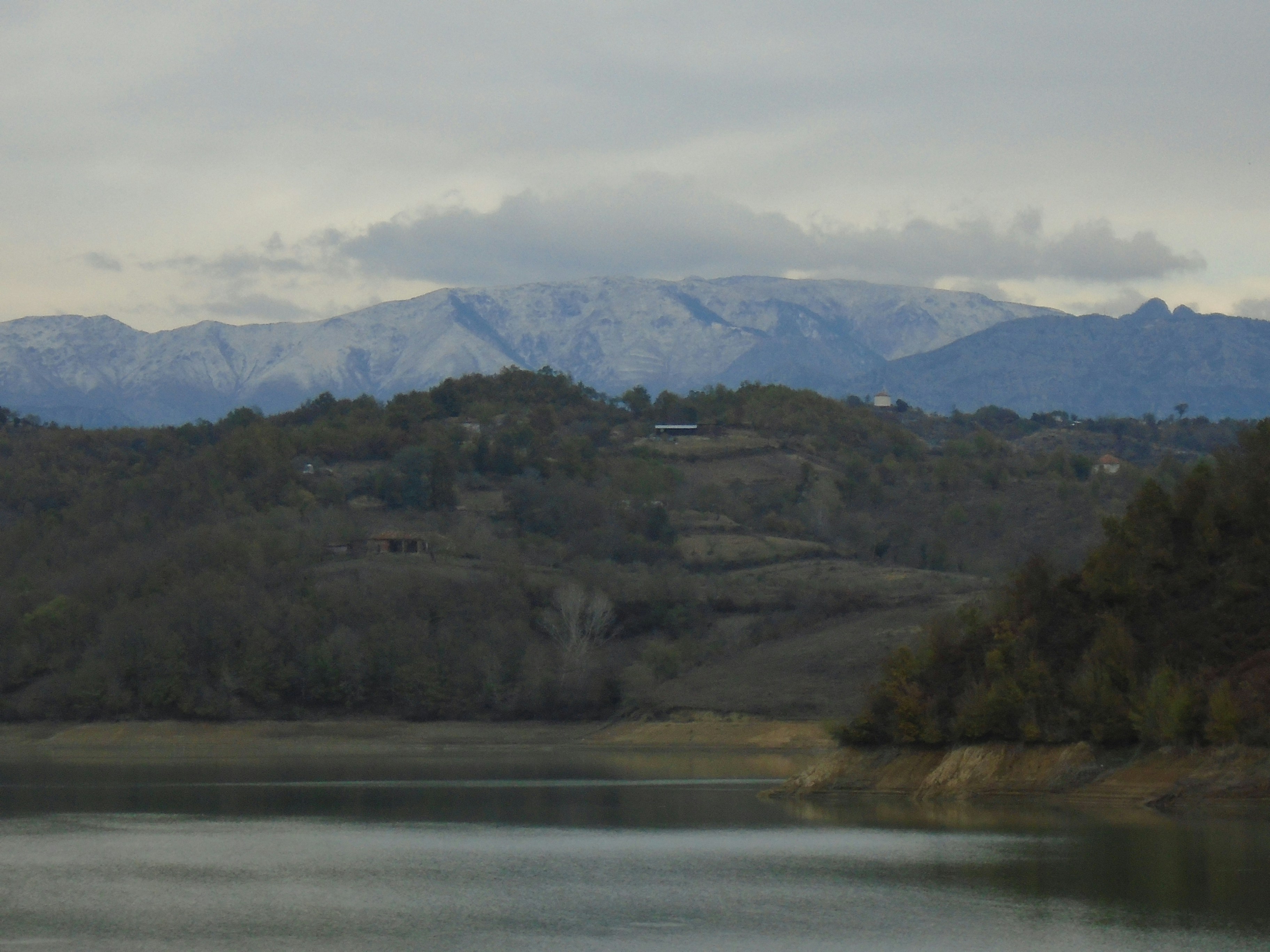 Serene landscape featuring a tranquil lake with snow-capped mountains in the background, surrounded by autumn foliage.