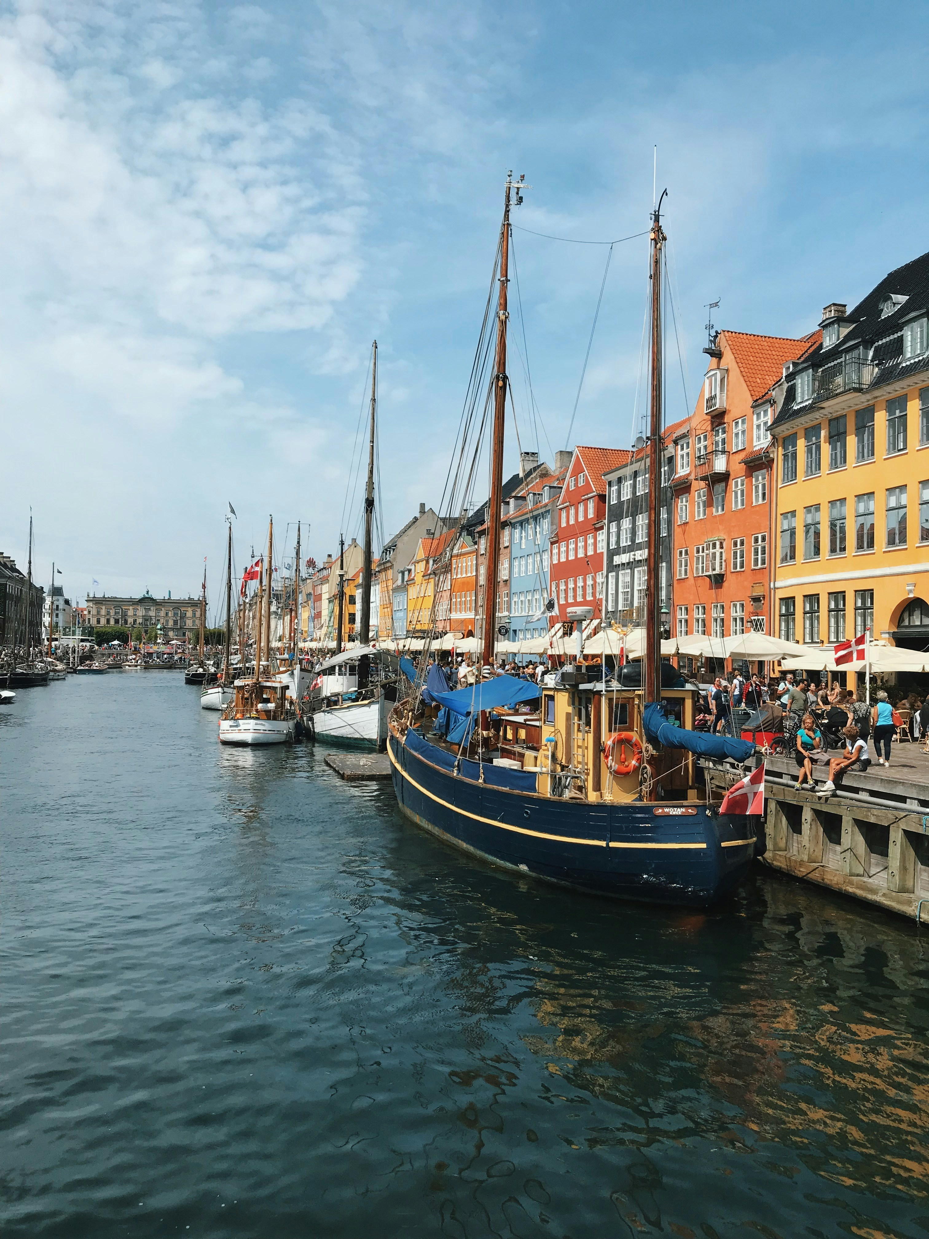 Vibrant harbor scene showcasing colorful buildings lining the waterfront, with sailboats and people enjoying the lively atmosphere. Perfect blend of urban charm and nautical life.