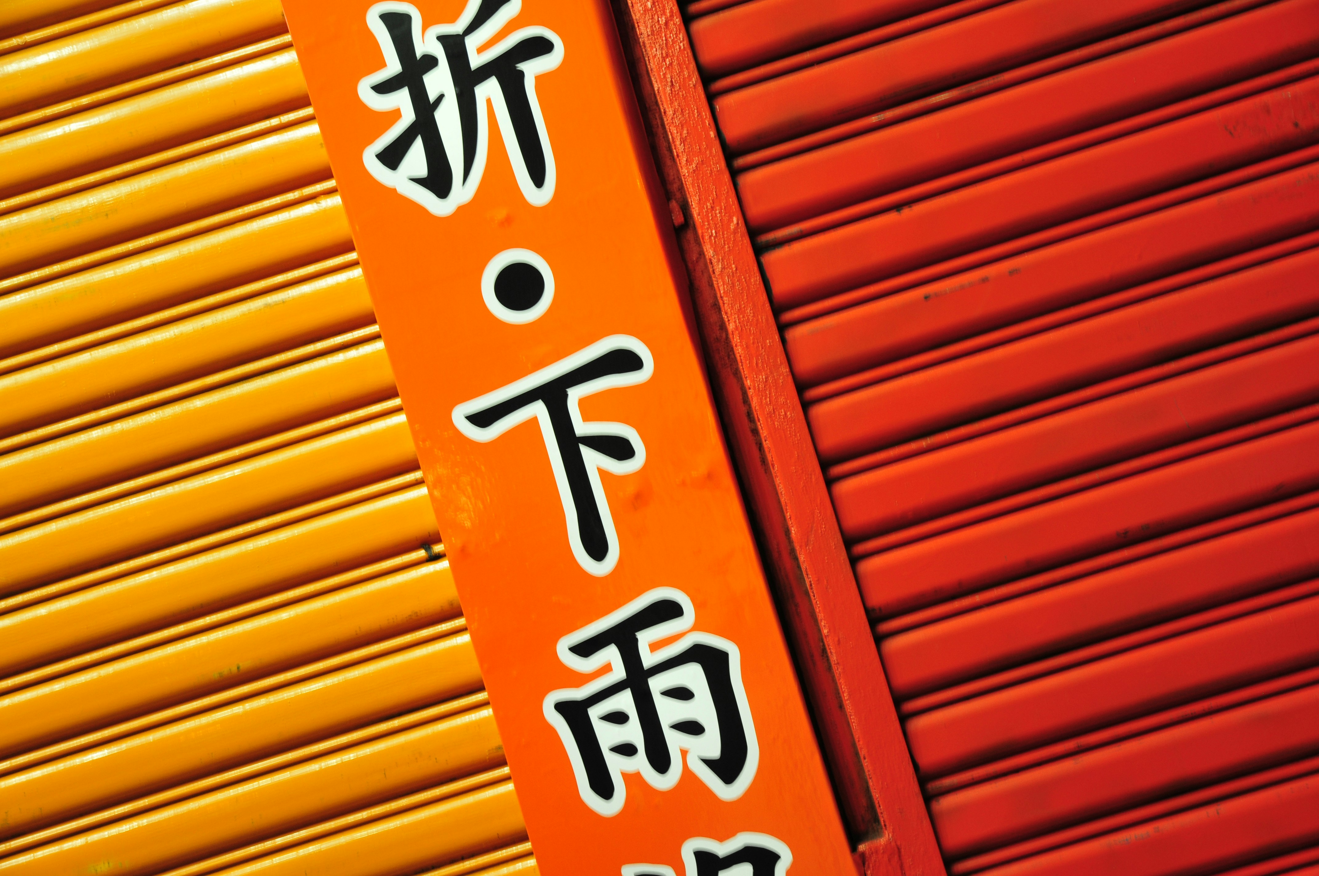 Bold orange sign with white text set against a backdrop of colorful vertical slats. The composition emphasizes urban aesthetics and cultural expression.