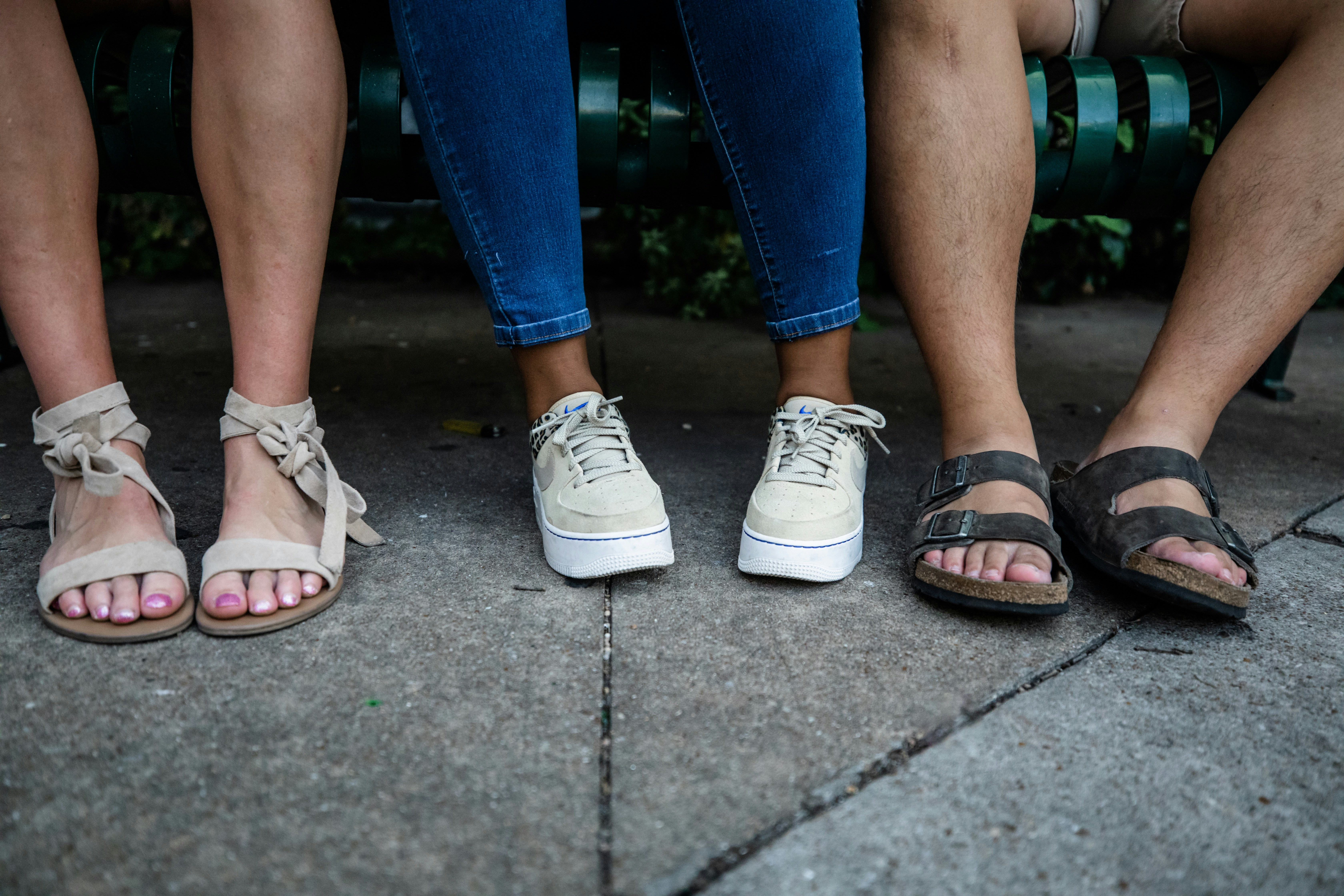 Feet in Sneakers: A Row of Varied Footwear on a Park Bench