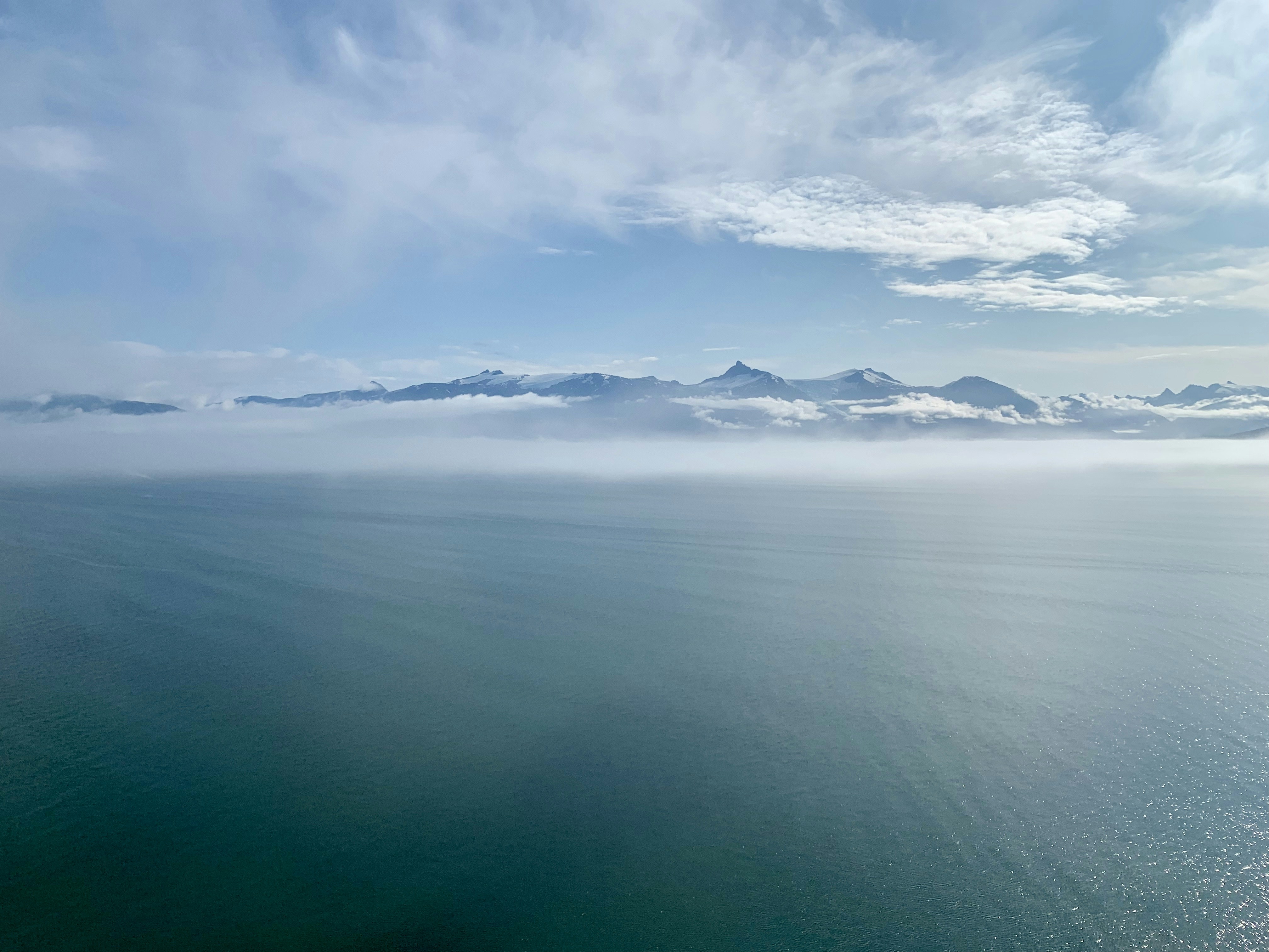 Mist-Rimmed Horizon: Snow-Capped Peaks Beyond a Glassy Sea