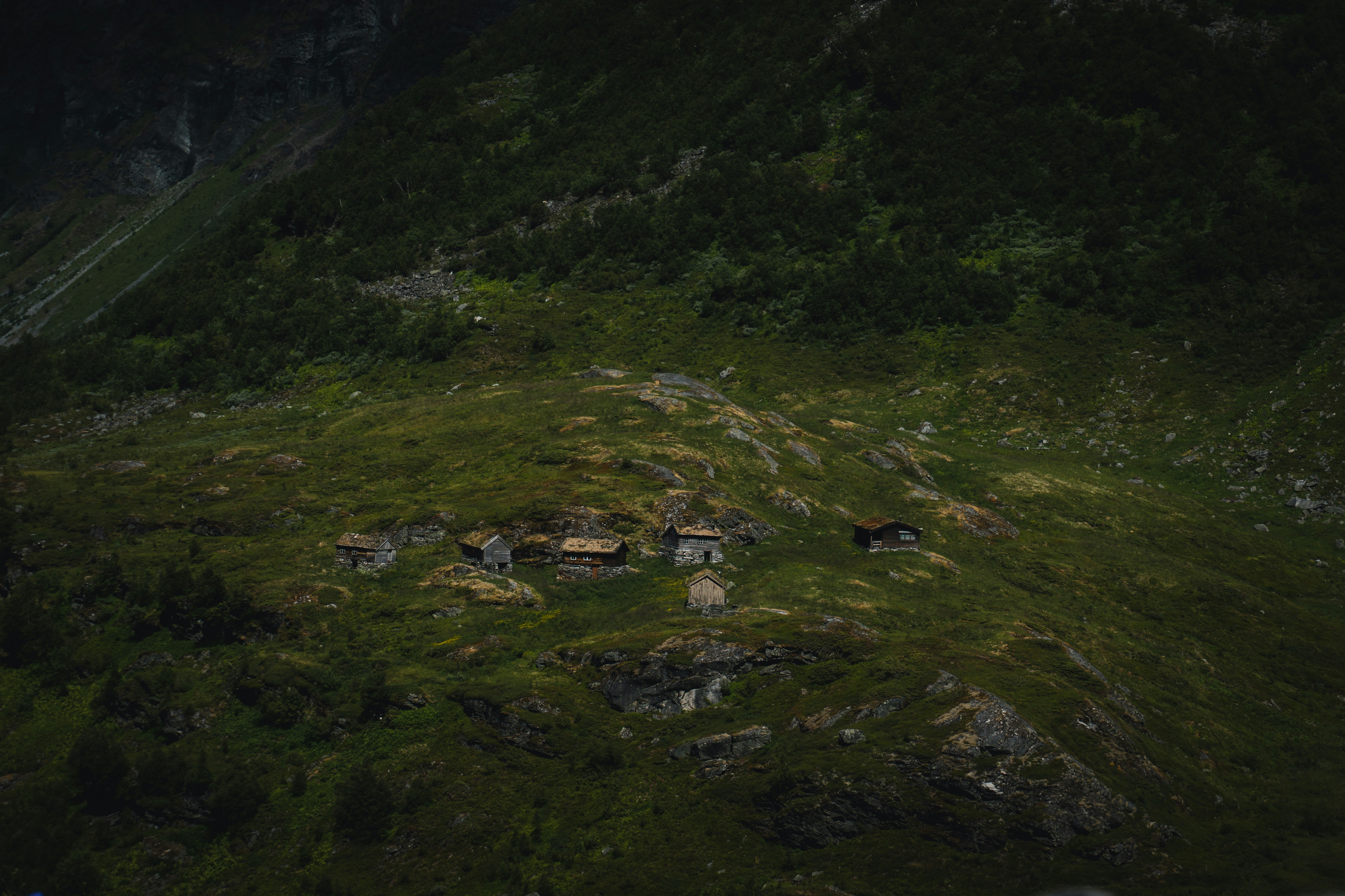 Scattered wooden cabins nestled in a lush, green mountain landscape, hinting at a forgotten past. The serene environment envelops the structures in nature's embrace.