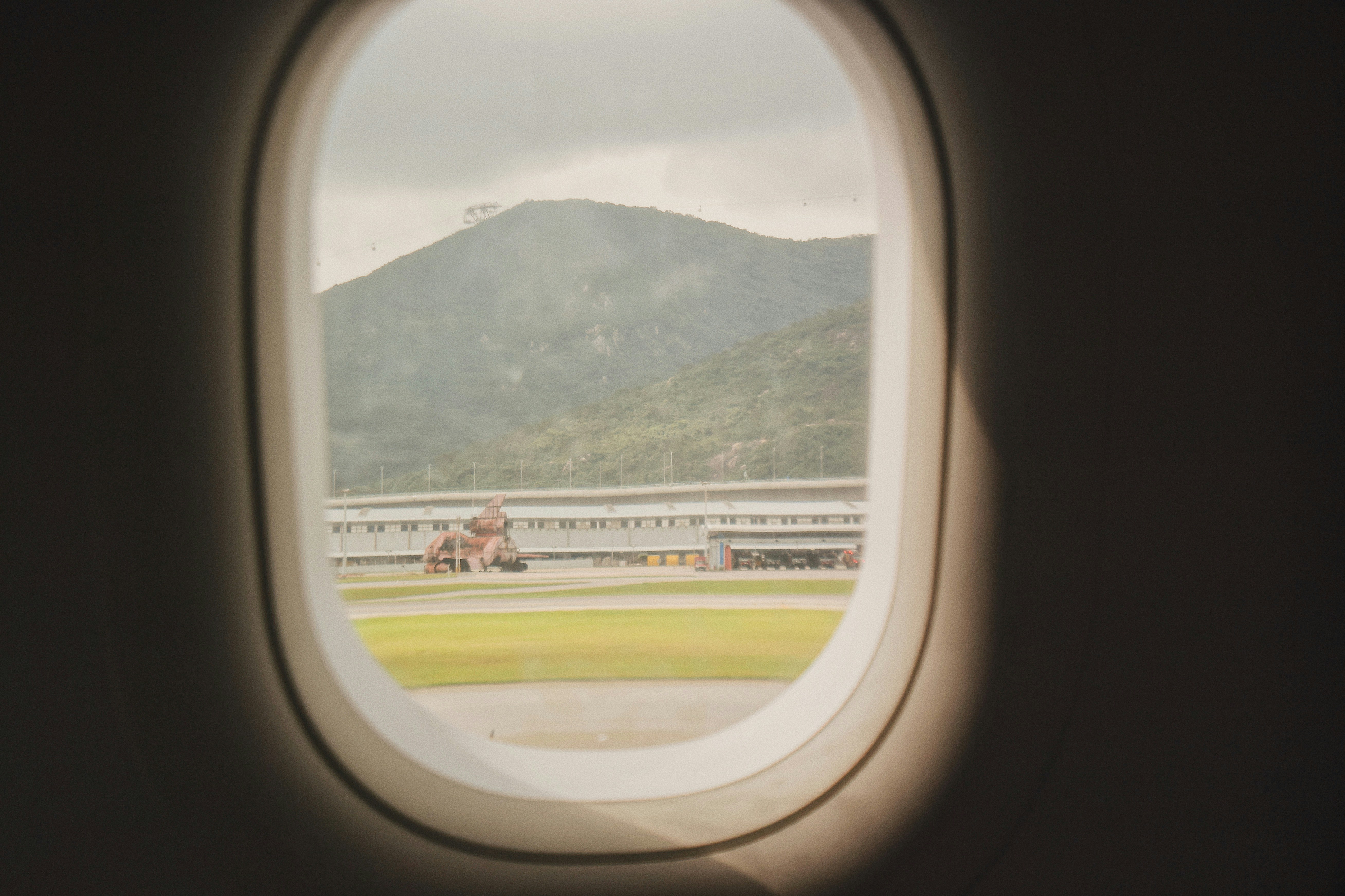 Airplane window framing a scenic view of a mountain with an airport runway in the foreground.