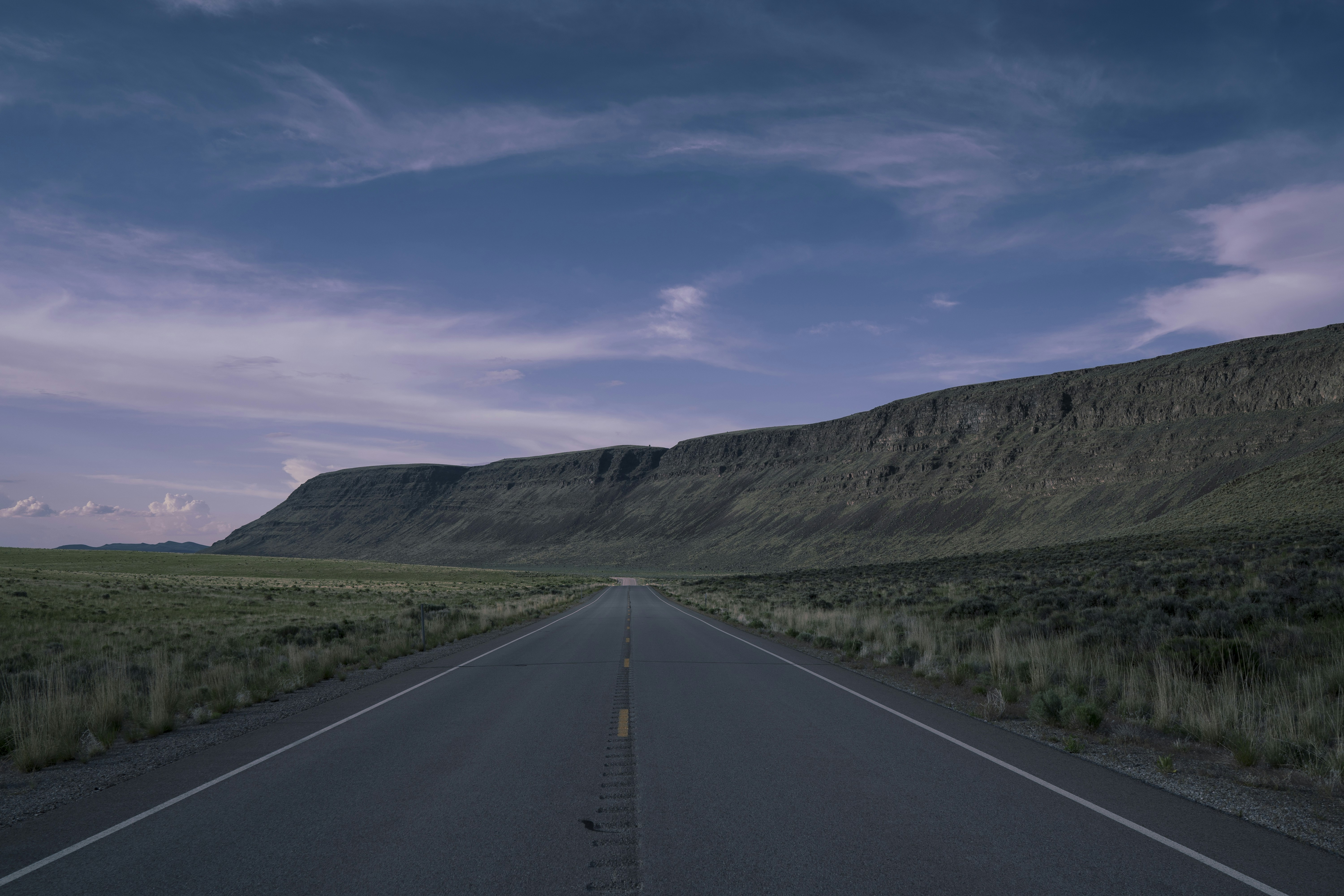 Lonely highway stretching towards distant mountains under a twilight sky, showcasing the vastness of the landscape.