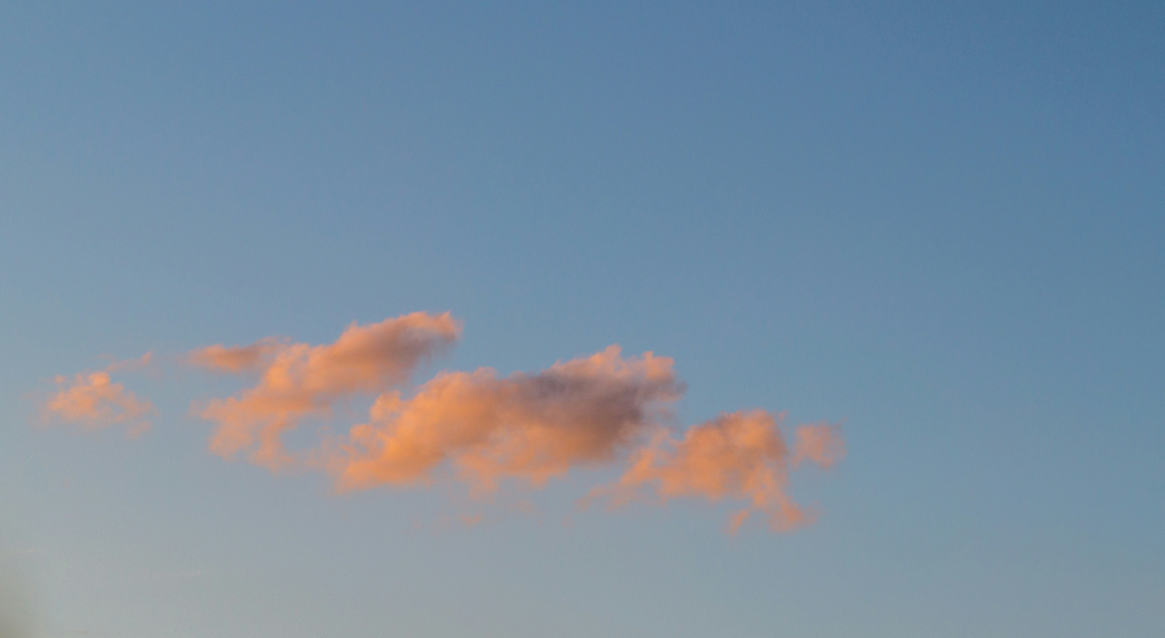 Soft pink clouds drift across a clear blue sky at dusk.