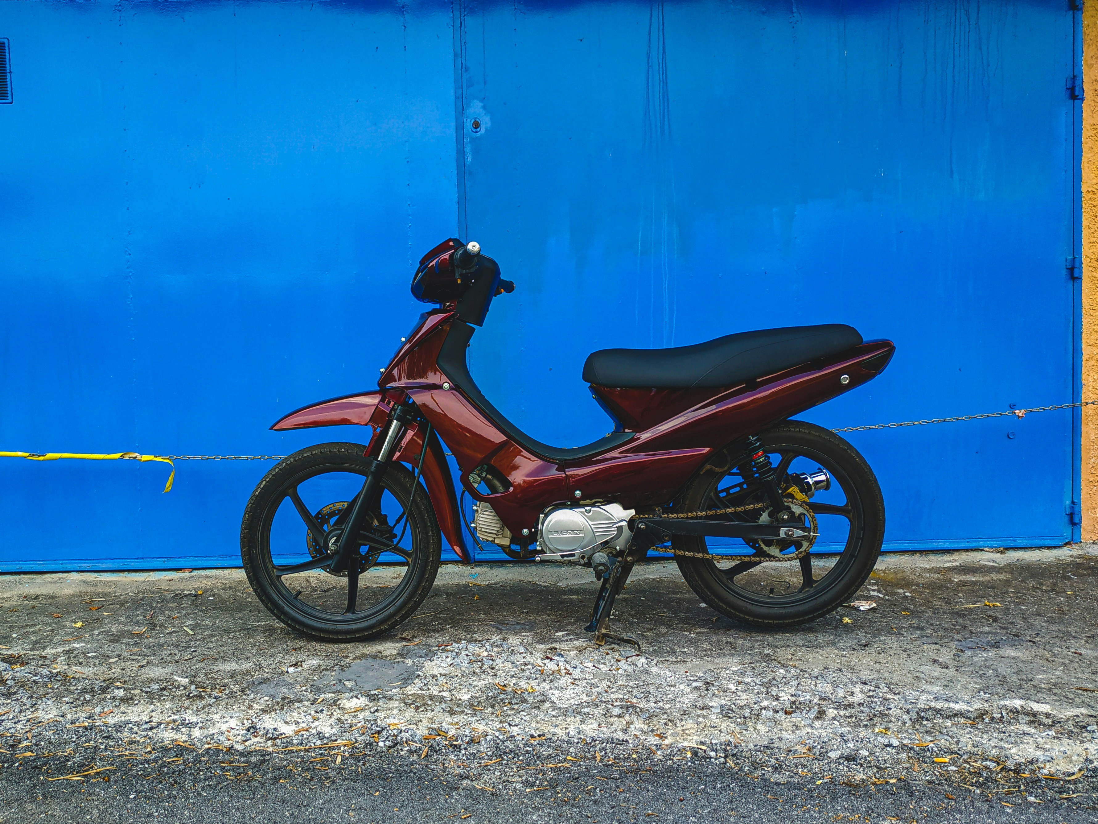 A maroon motorcycle stands against a bright blue wall, highlighting its sleek design and urban setting.