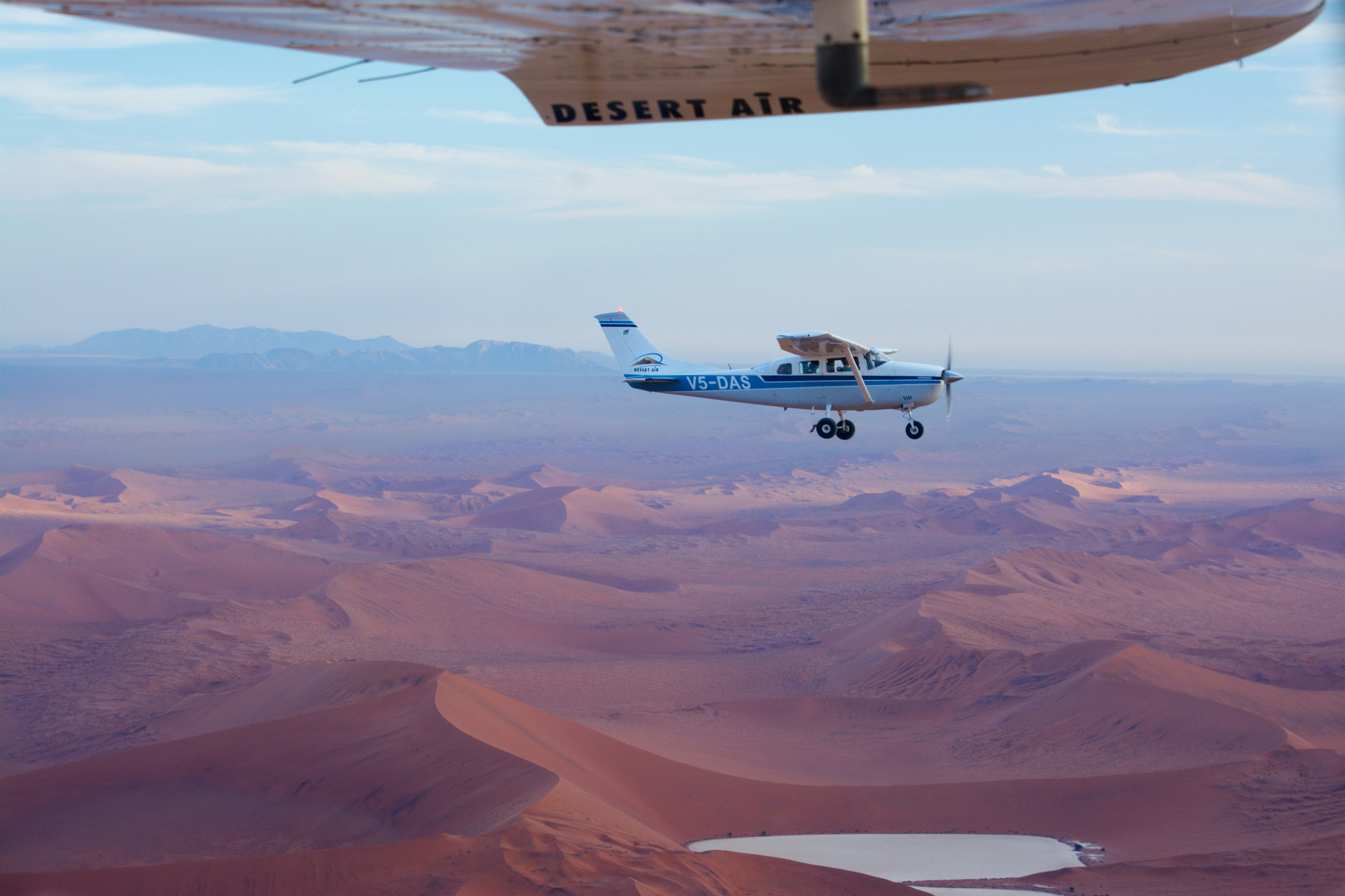Desert Skies: A Lone Bush Plane Gliding Above Rust-Red Dunes