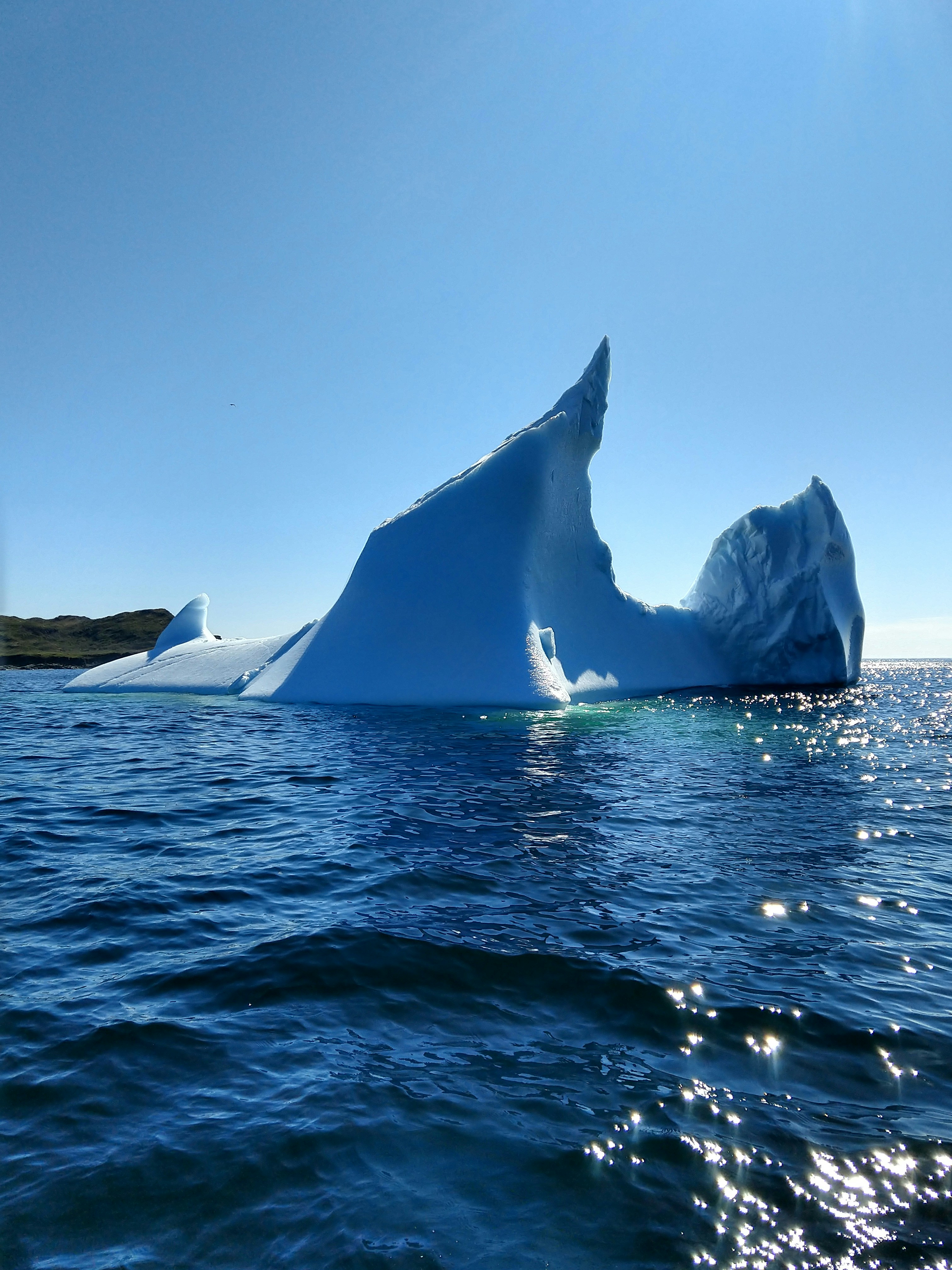 Majestic iceberg rising from the ocean, illuminated by bright sunlight, with shimmering water reflecting its form.