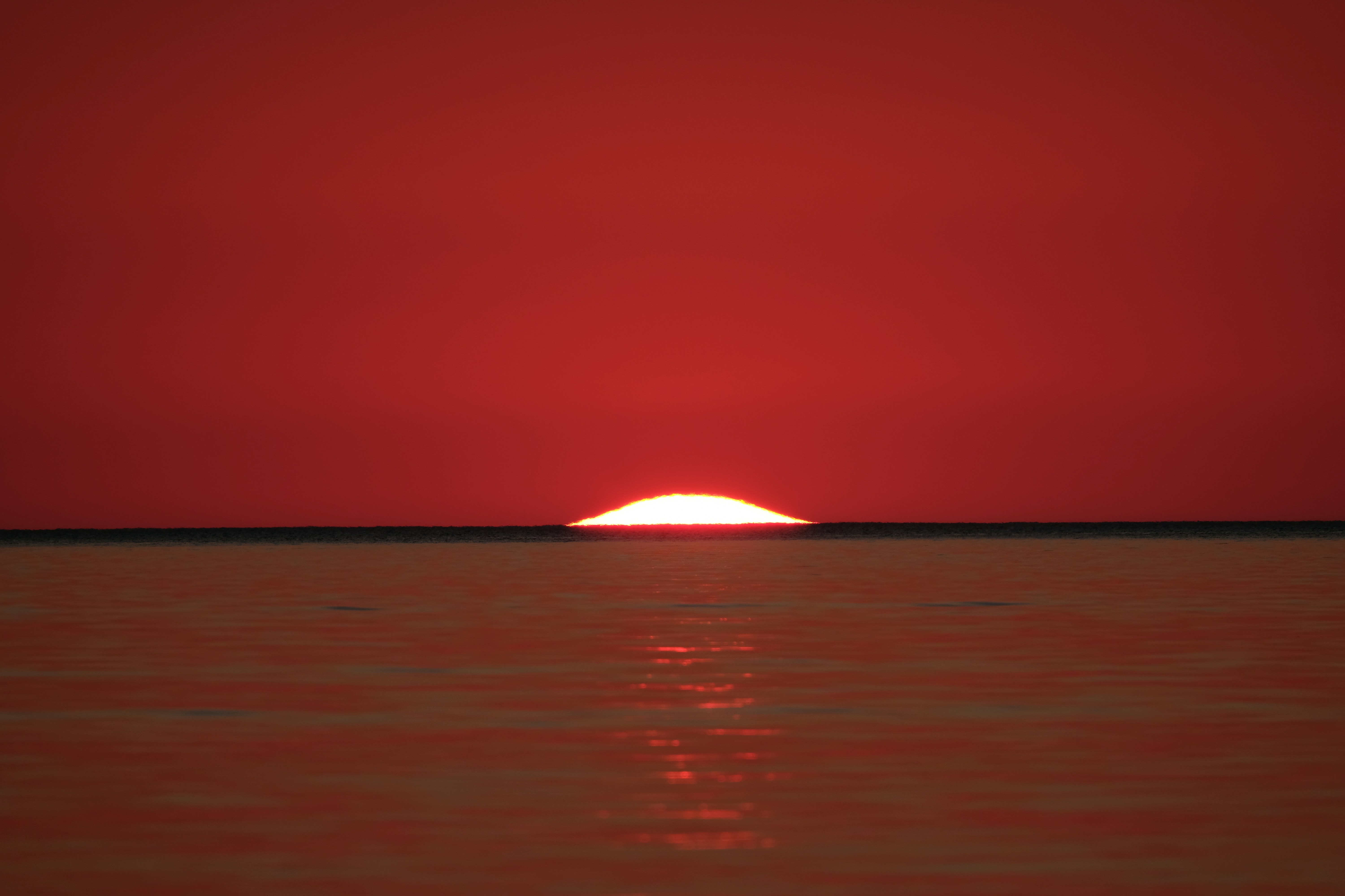 Crimson Horizon: Sun Sets Over a Glassy Red Sea