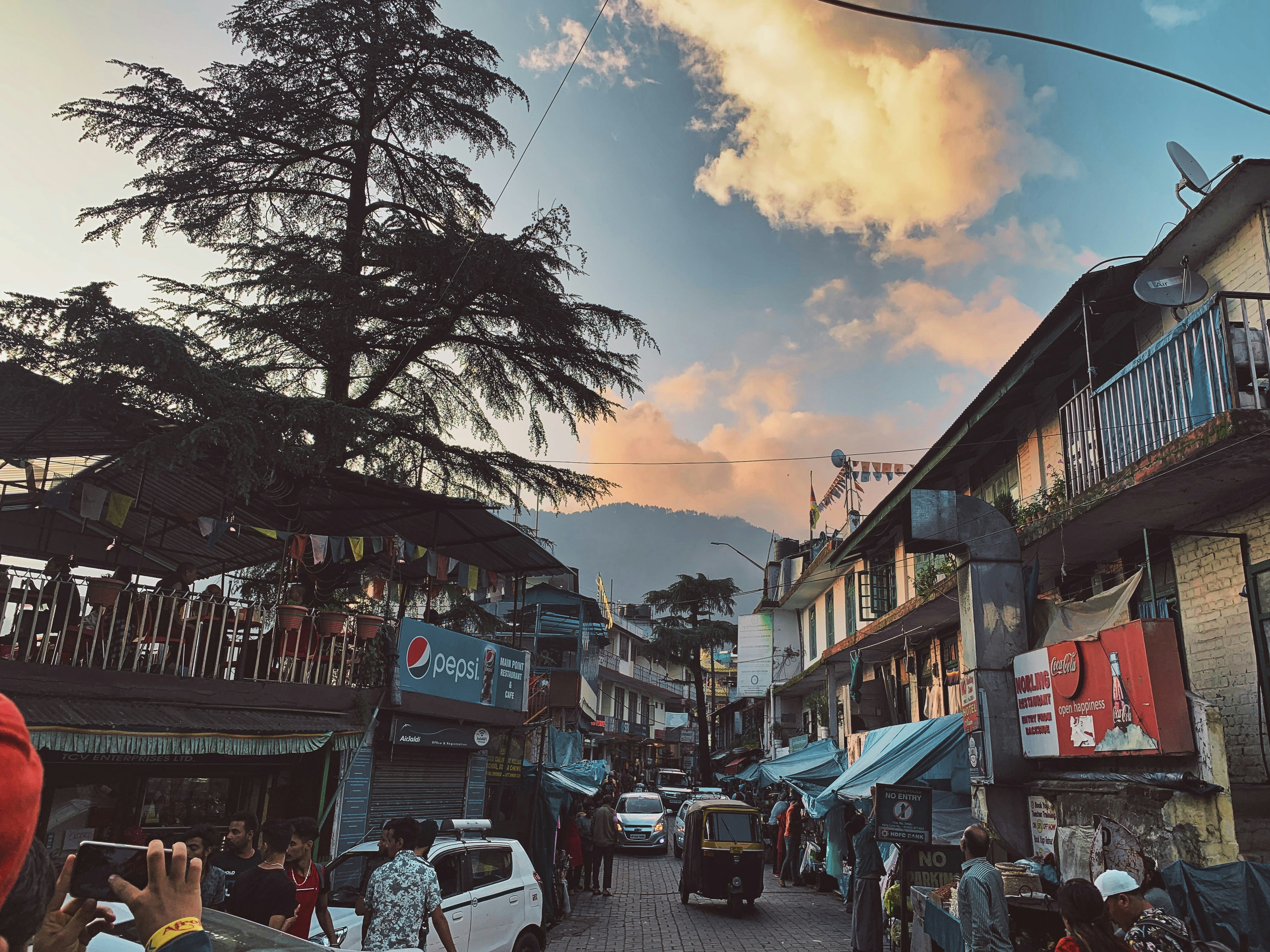 Bustling street scene in a mountain town during twilight, showcasing shops, vehicles, and a vibrant sky adorned with clouds.