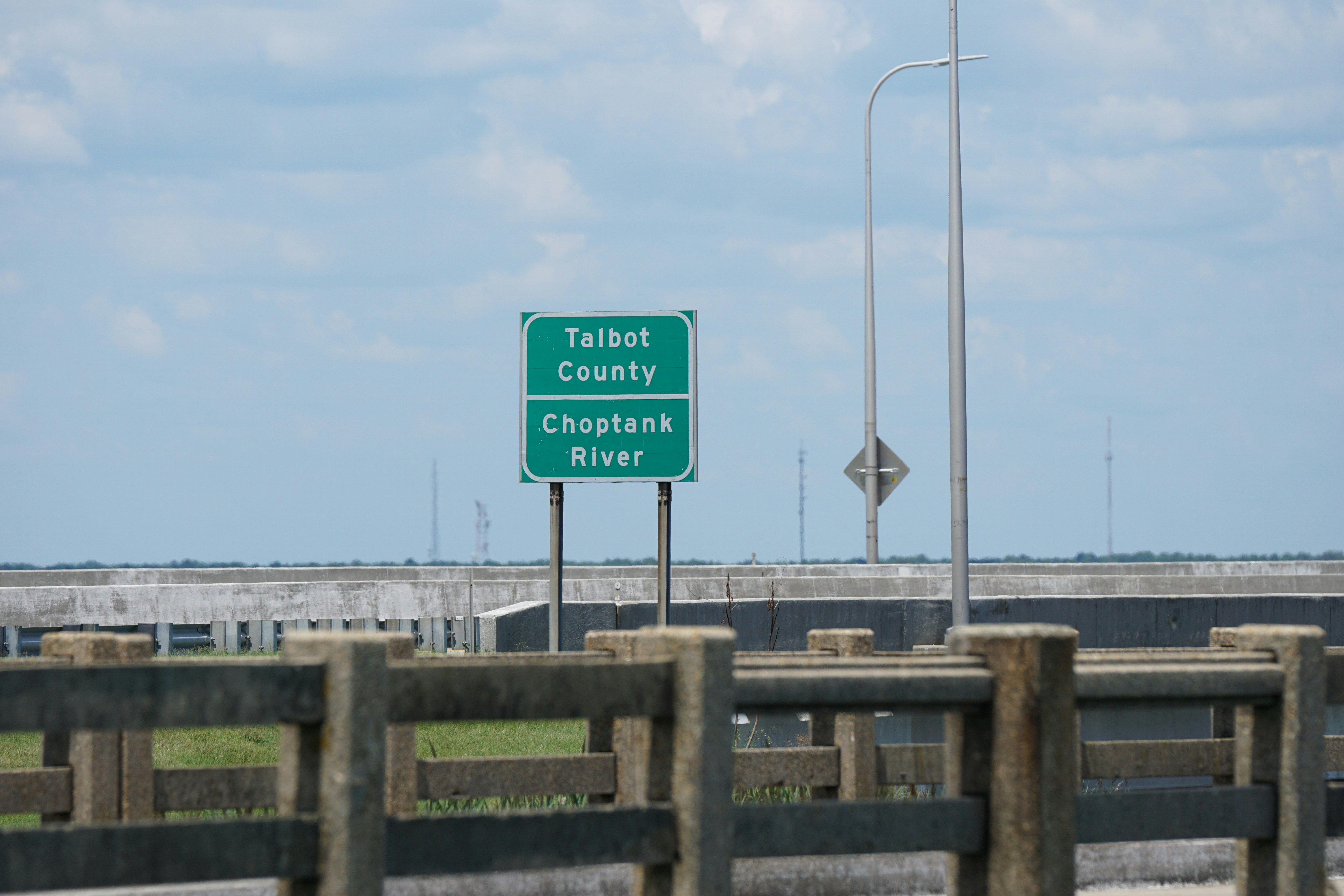 Road sign indicating Talbot County and Choptank River, framed by a wooden fence and open landscape. 