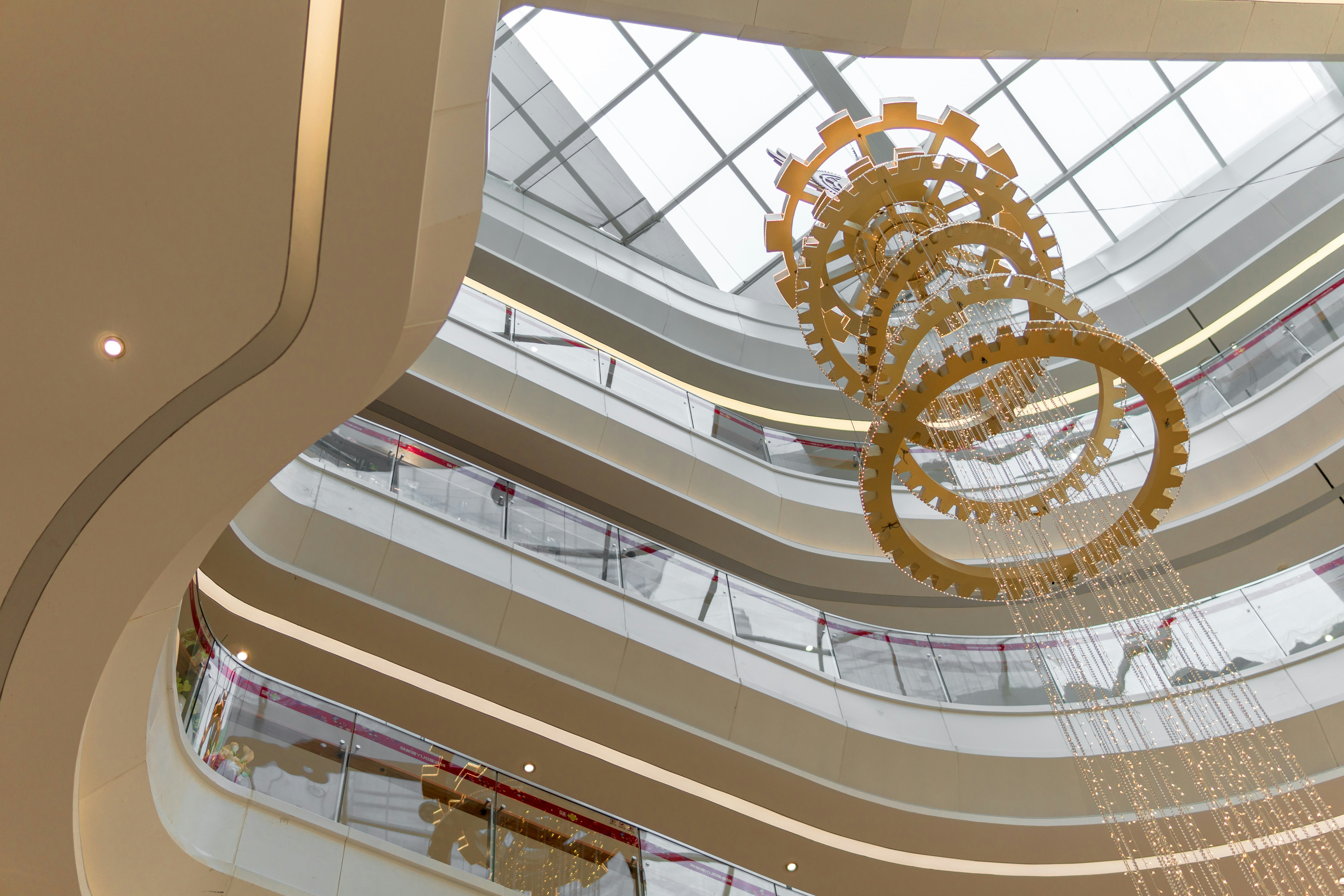 Intricate chandelier suspended in a contemporary atrium, showcasing smooth lines and natural light filtering through the glass ceiling.